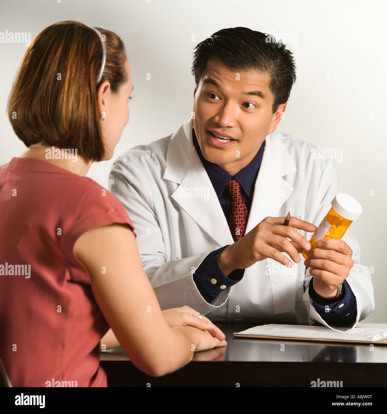 Asian American male doctor explaining medication to Caucasian female ...