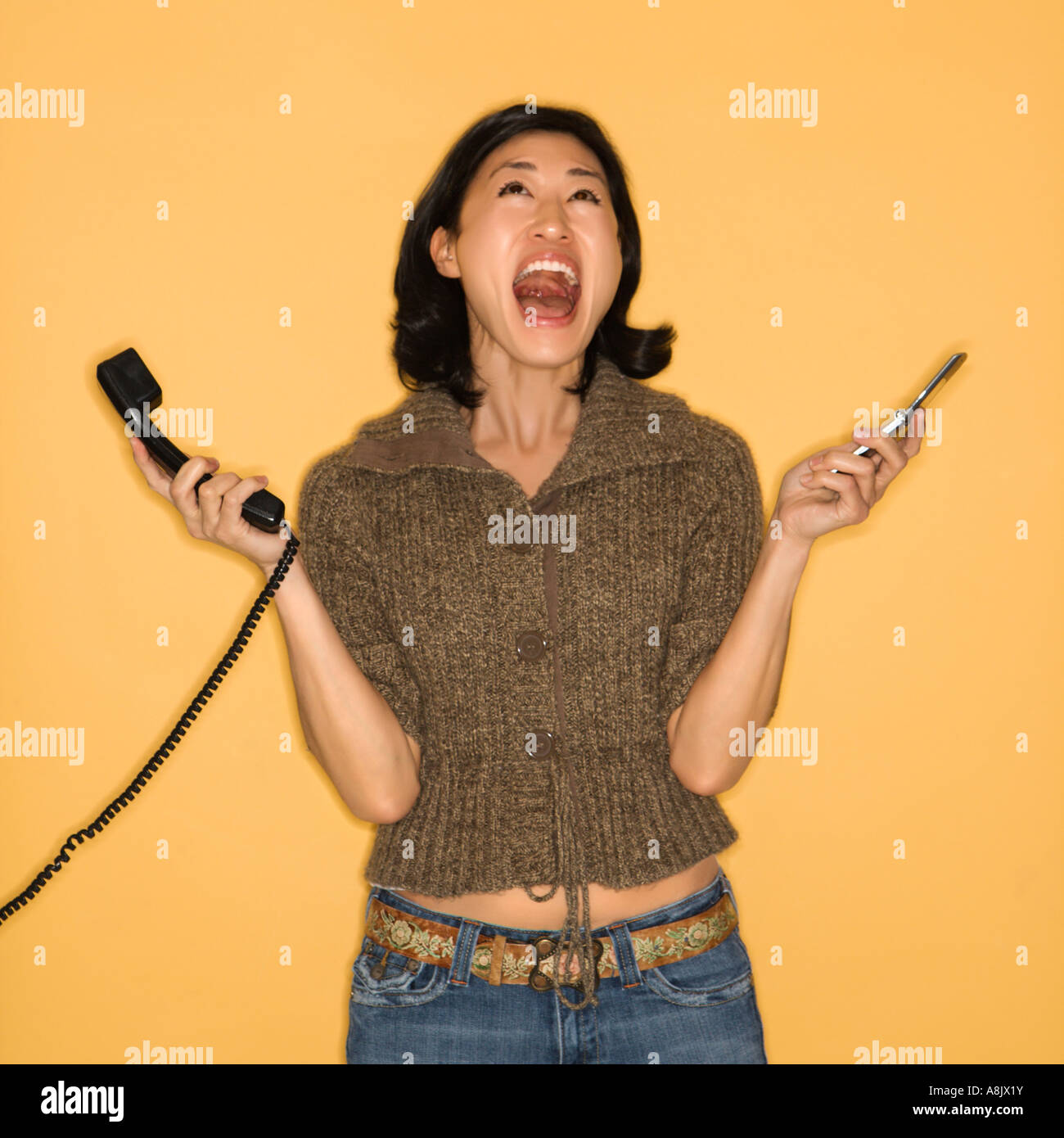 Pretty mid adult Asian woman holding telephone and cellphone with mouth ...