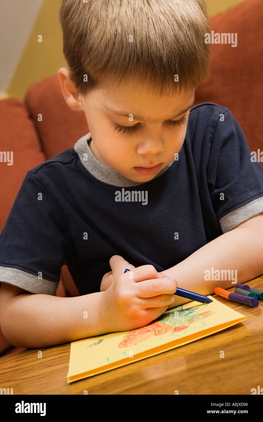 Caucasian boy drawing on yellow paper with crayons Stock Photo - Alamy