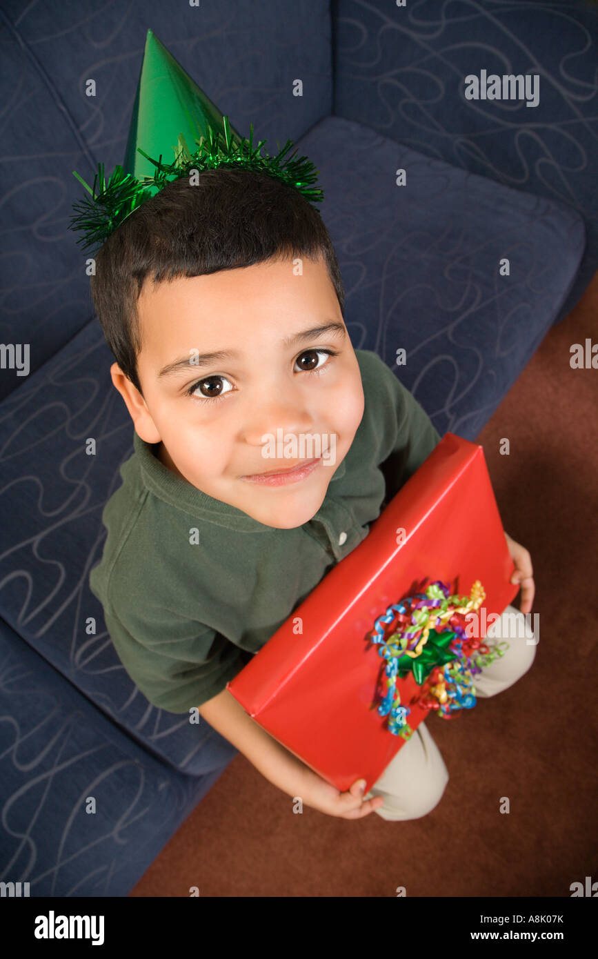 Hispanic boy wearing party hat holding birthday present looking up at ...