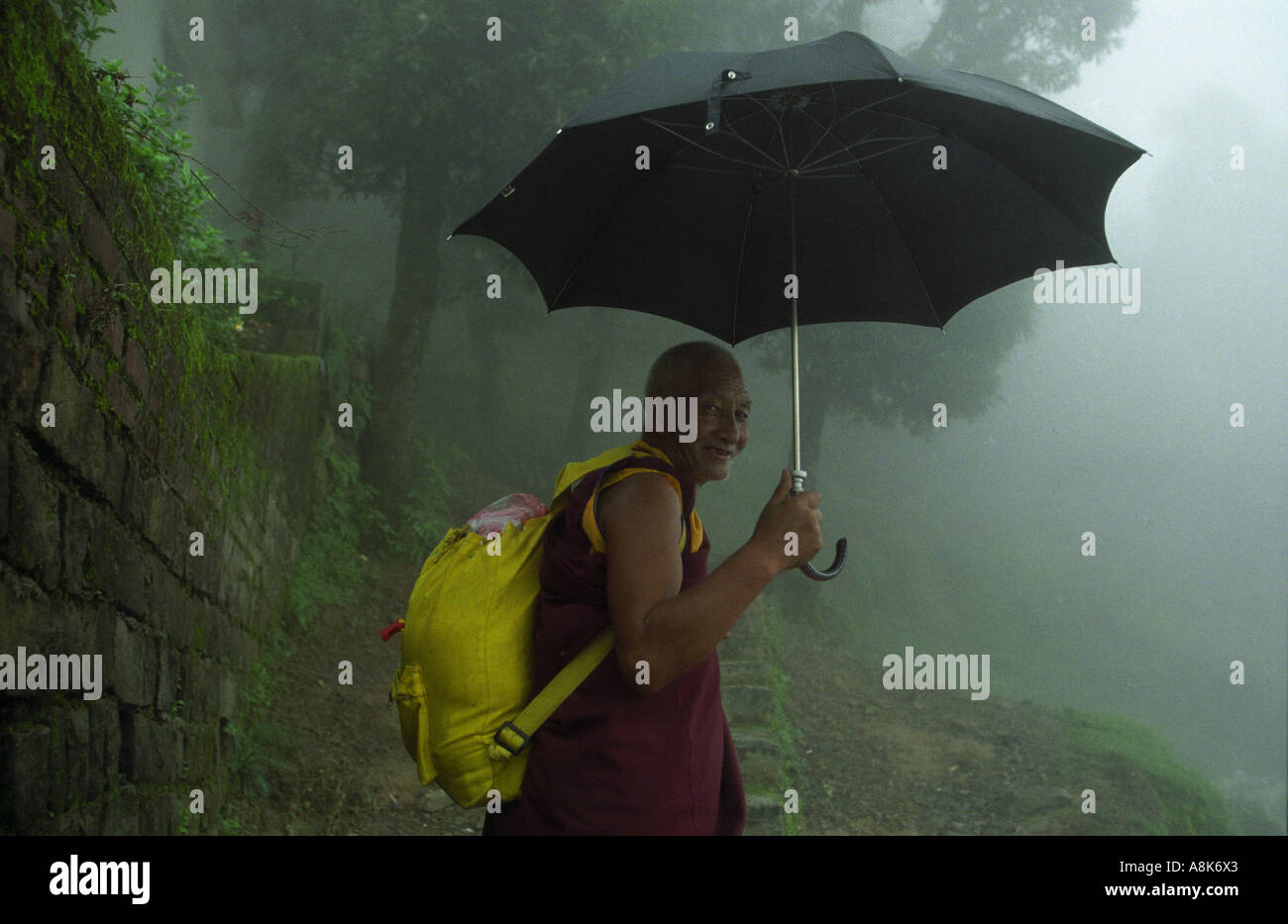 A Tibetan monk walks with an umbrella and a welcoming gesture in ...