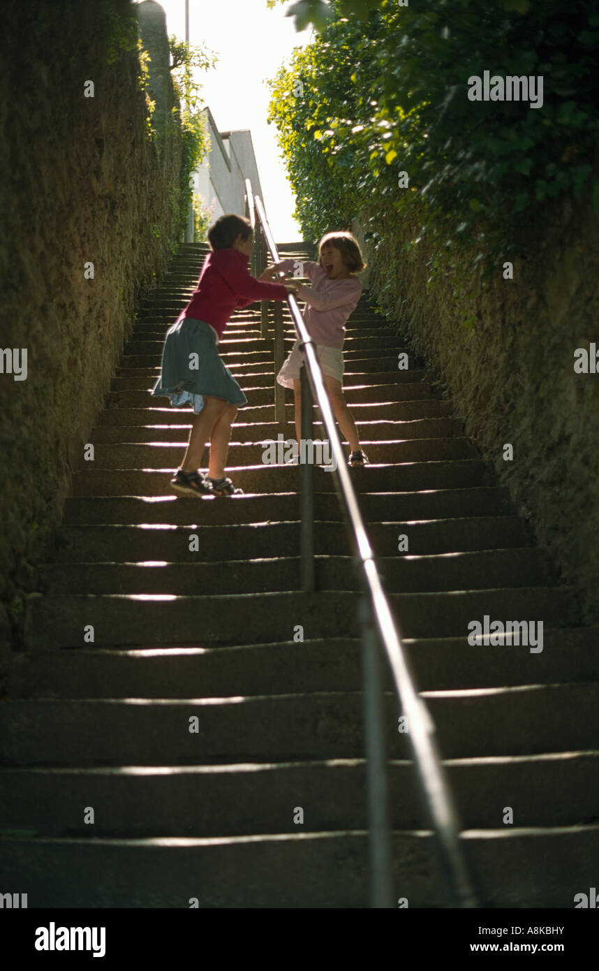 Two young children playing on steps swinging on the railings Stock ...