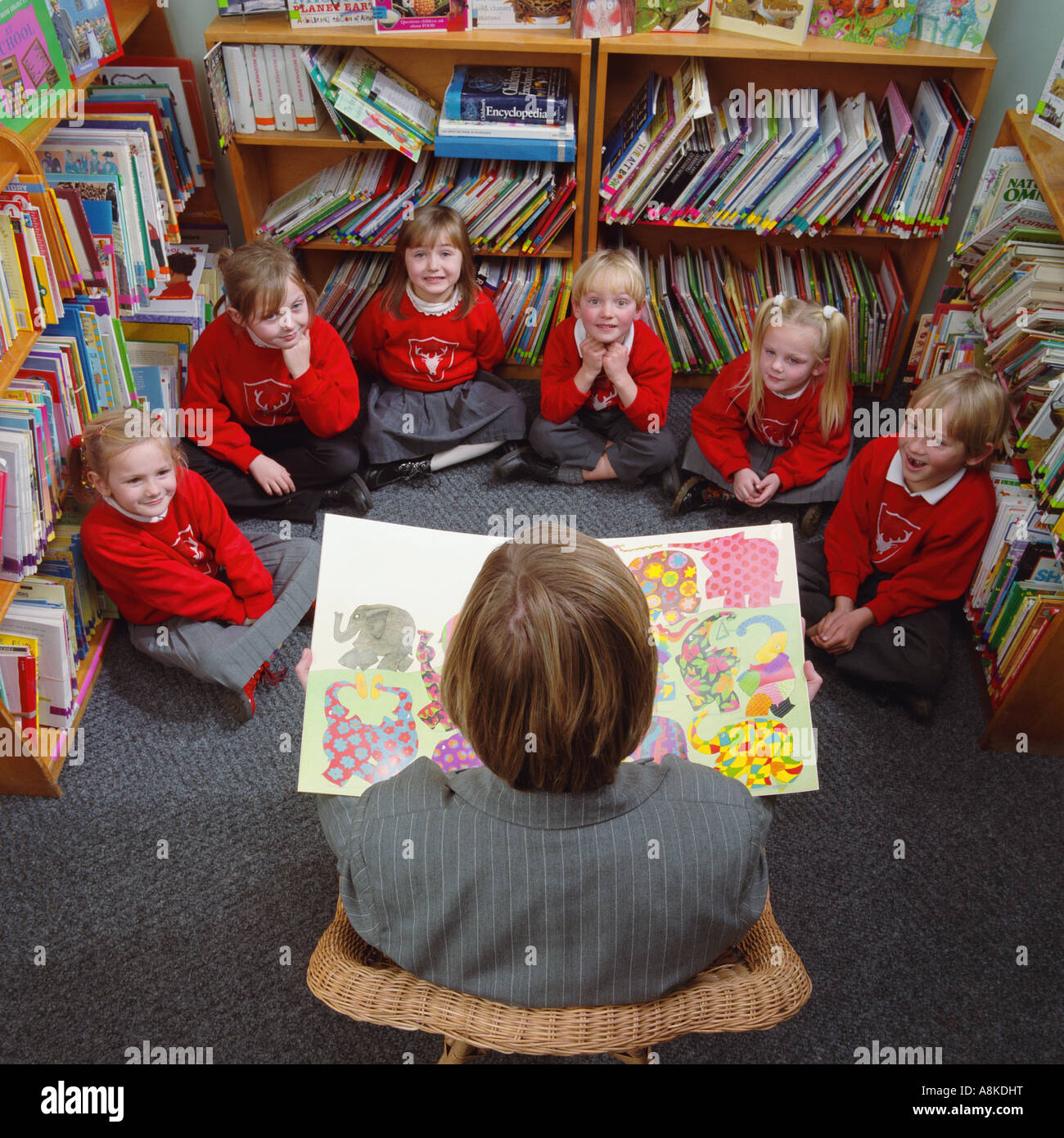 A teacher reading a book to a group of children children concentrating ...