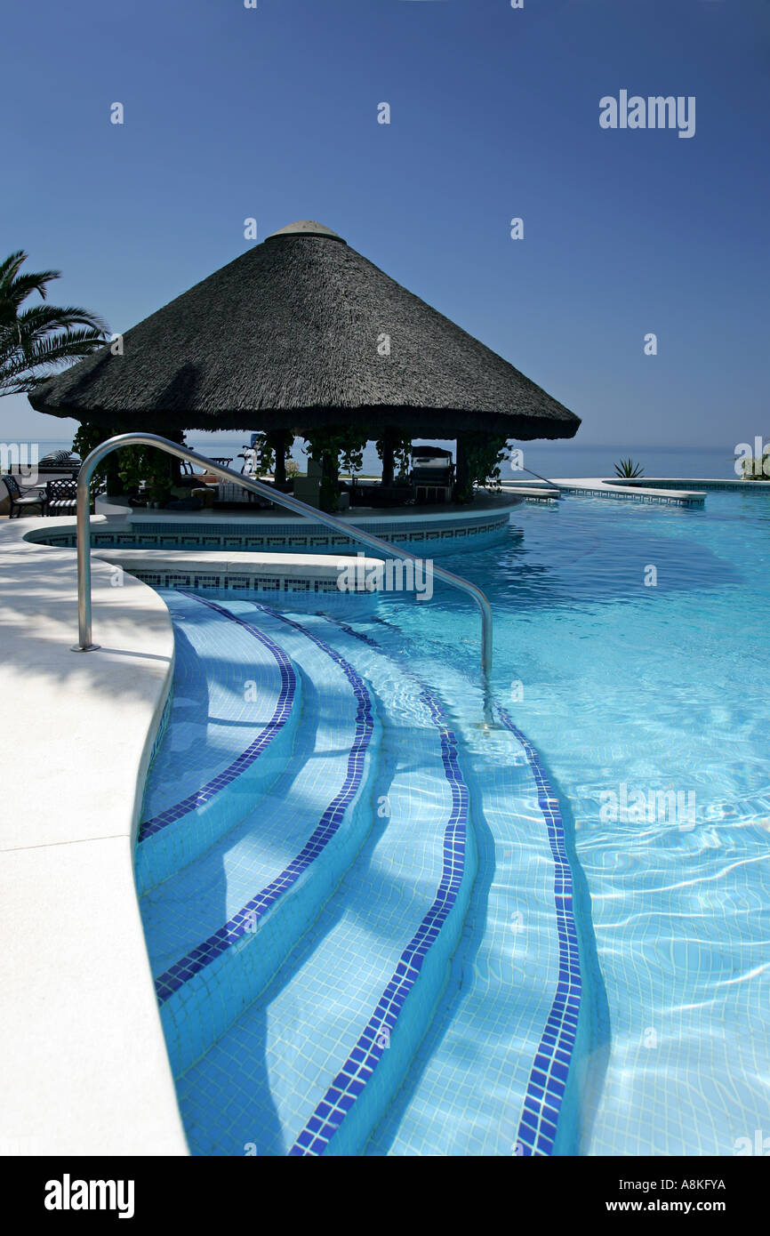 Tiki hut and bar by steps of swimming pool of luxury hotel on a bright ...