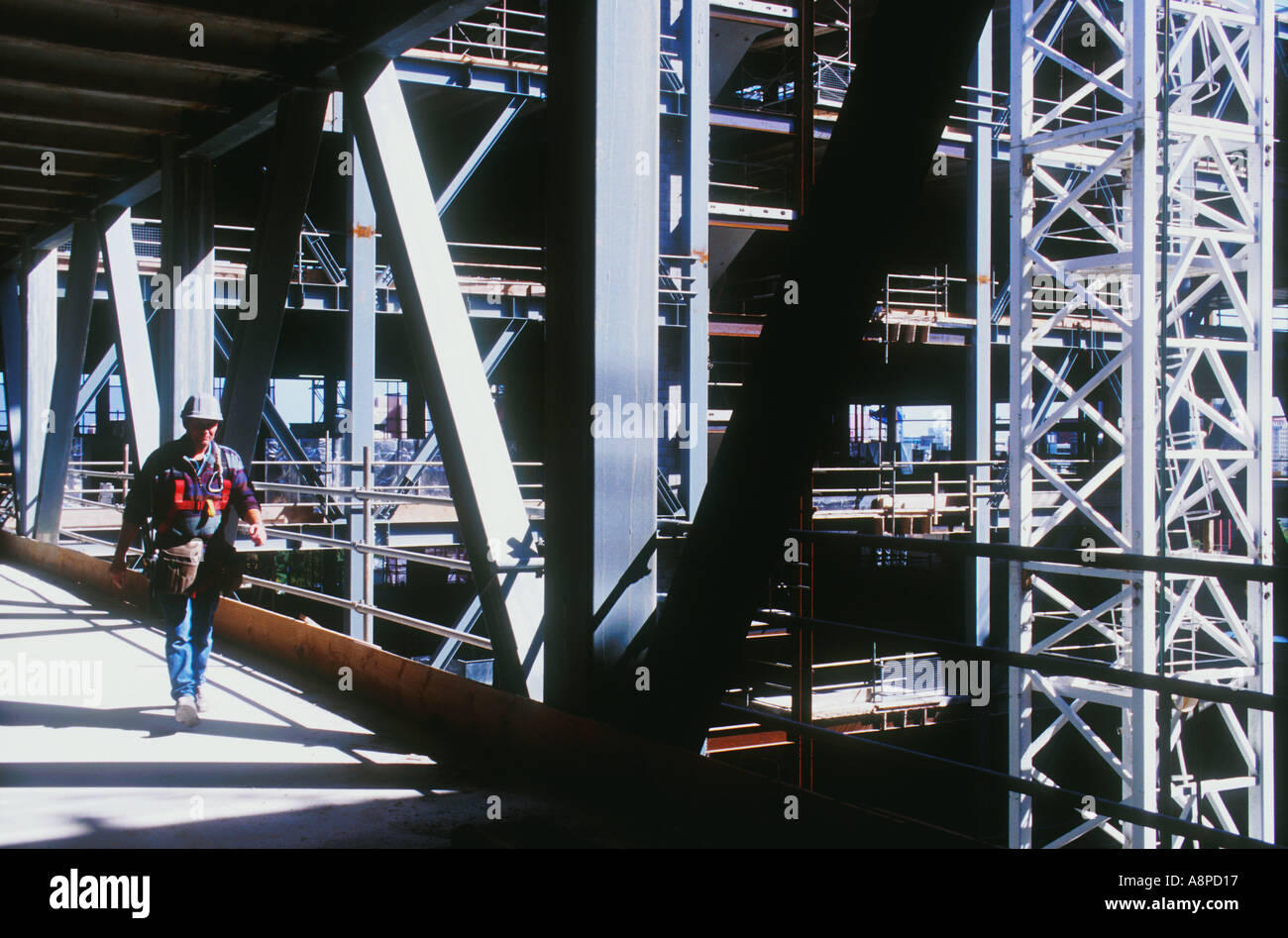 A construction worker wearing a safety harness and hard hat walking on ...