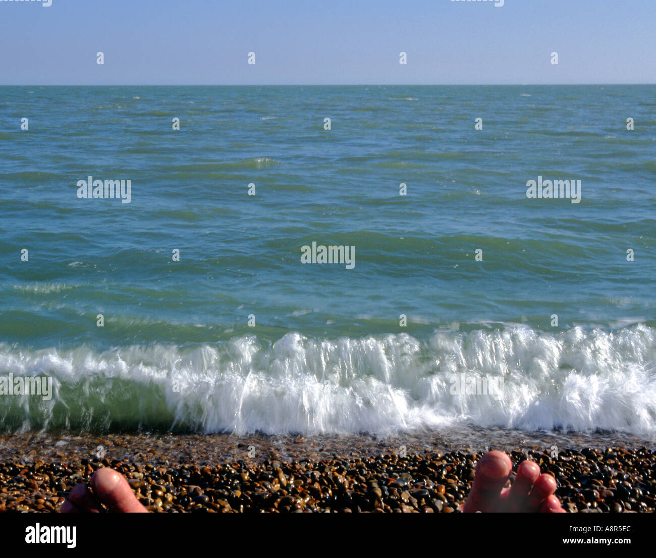 Photographer s feet toes shot of shingle beach sea and wave breaking ...
