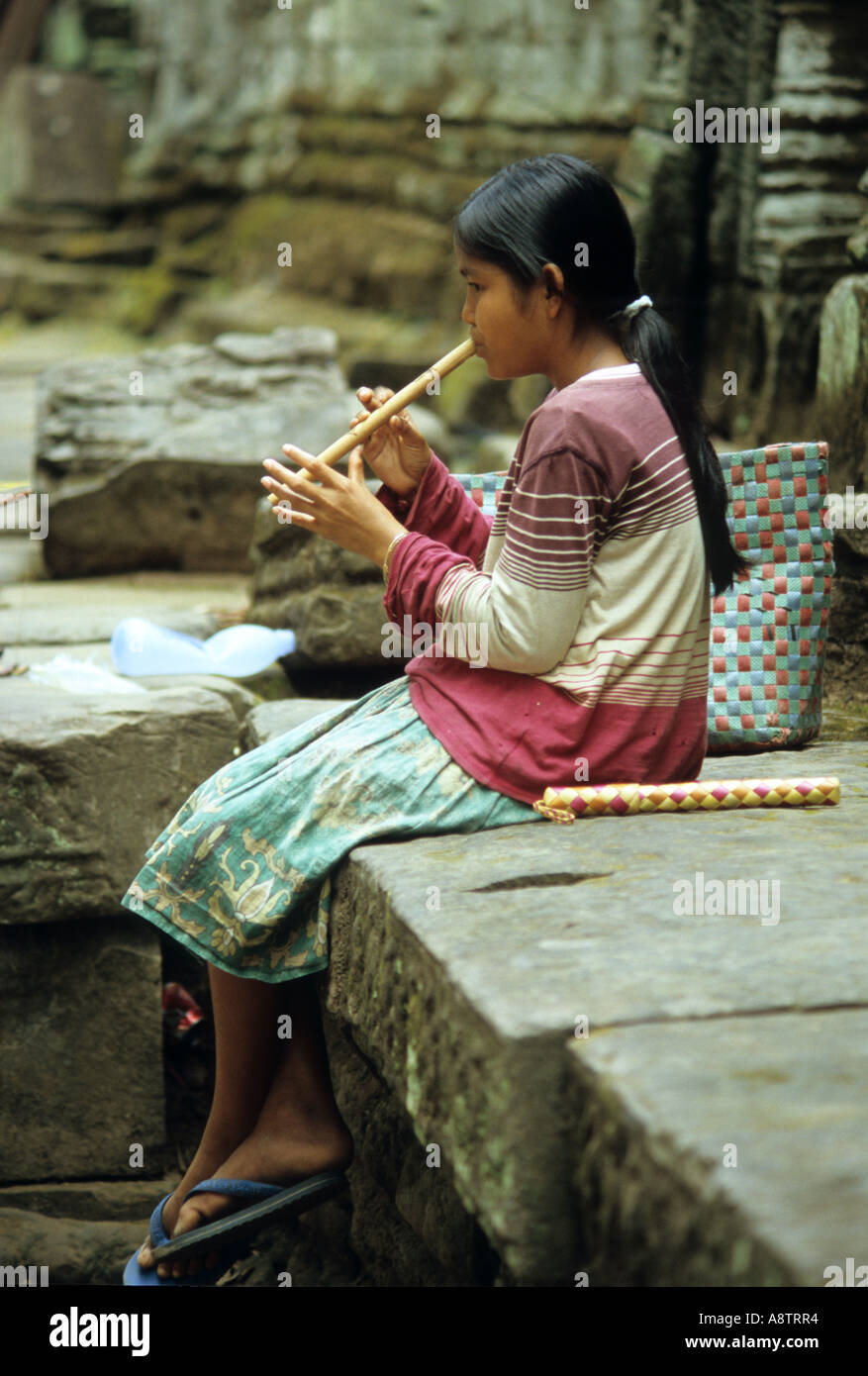 Khmer girl playing flute sitting on a wall at Ta Prohm Temple, Cambodia ...