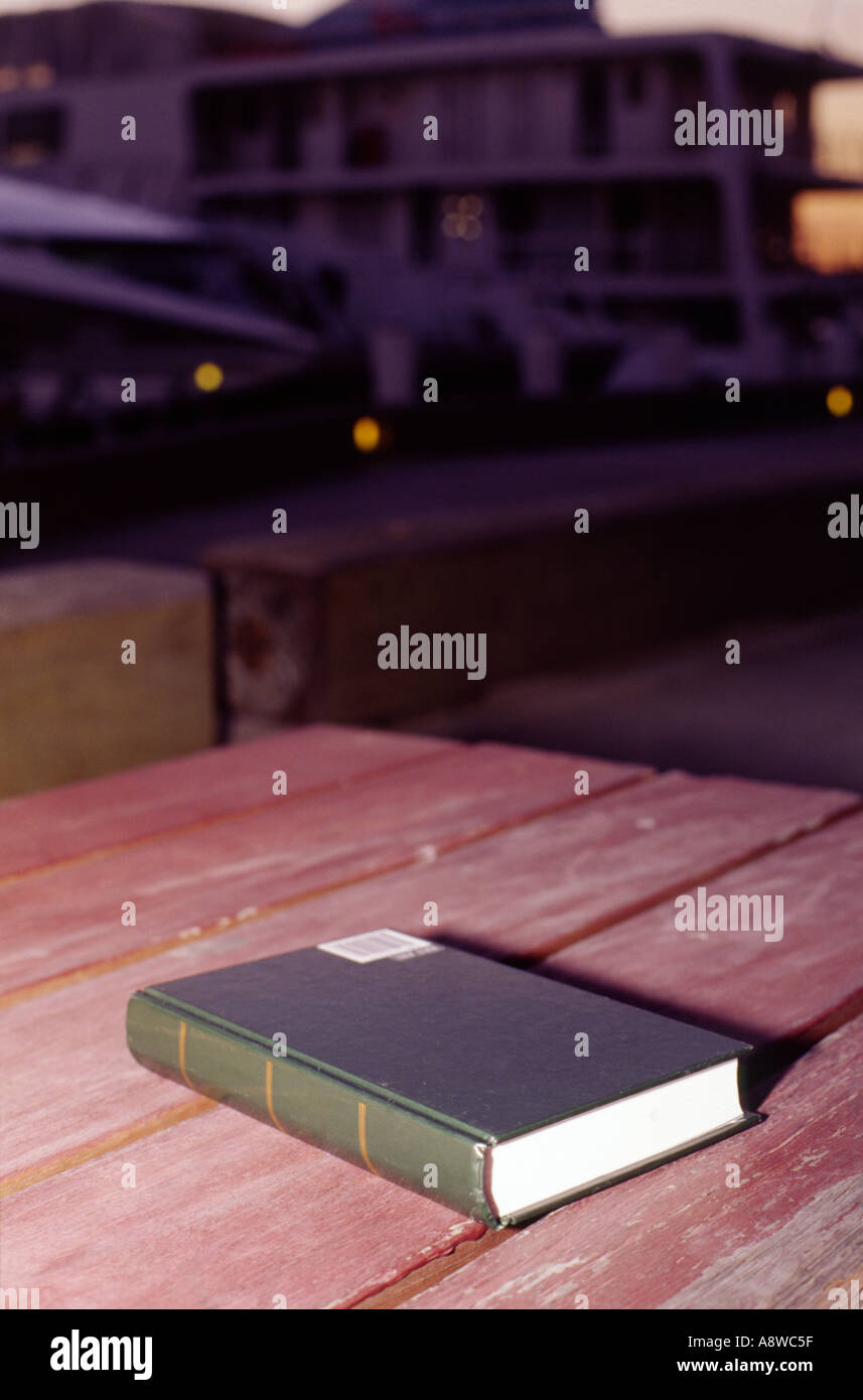 Green hardcover book on a wooden bench at a harbour wharf with carnival ...