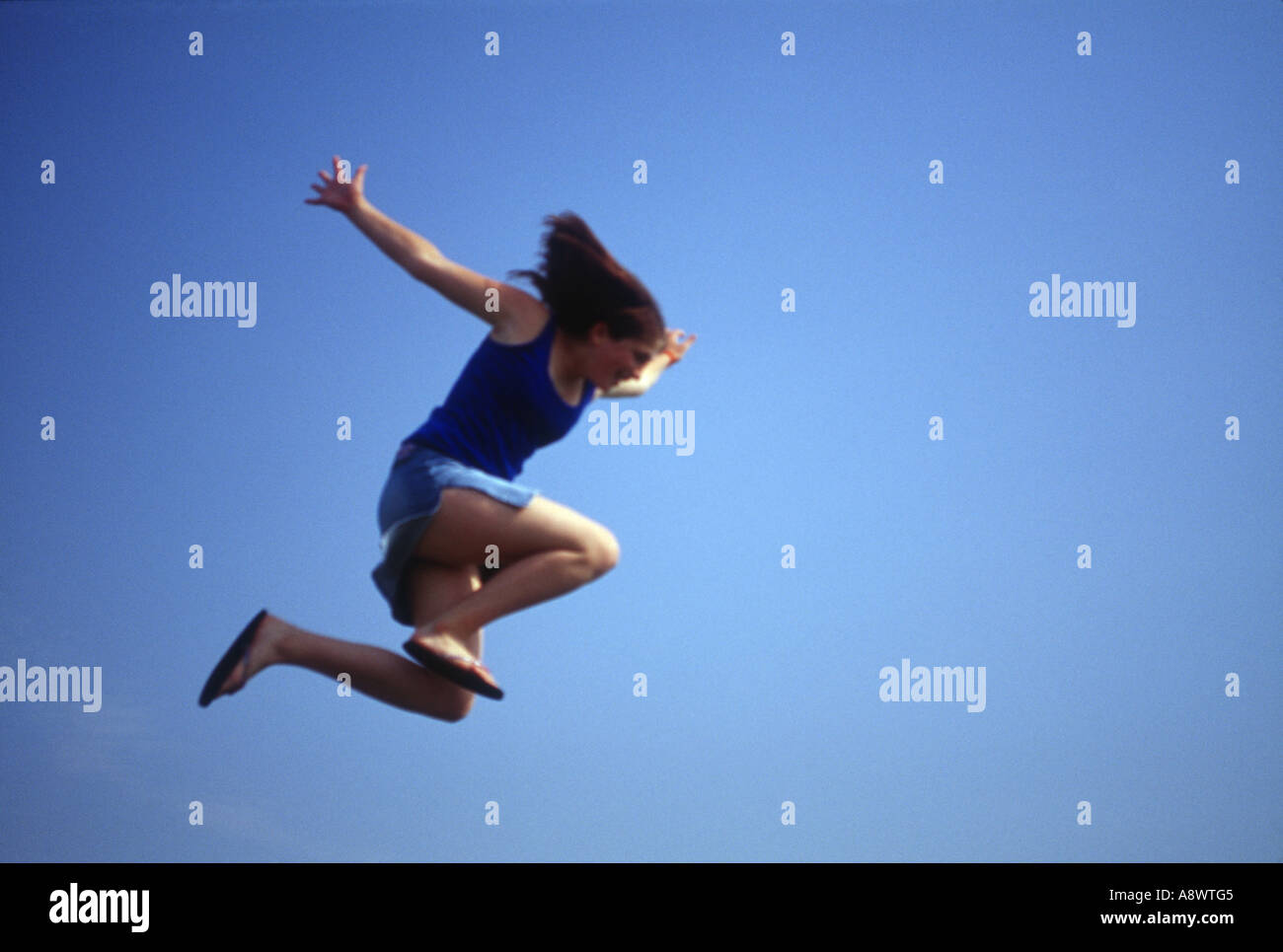 Teenage girl jumping against a clear blue sky Stock Photo - Alamy