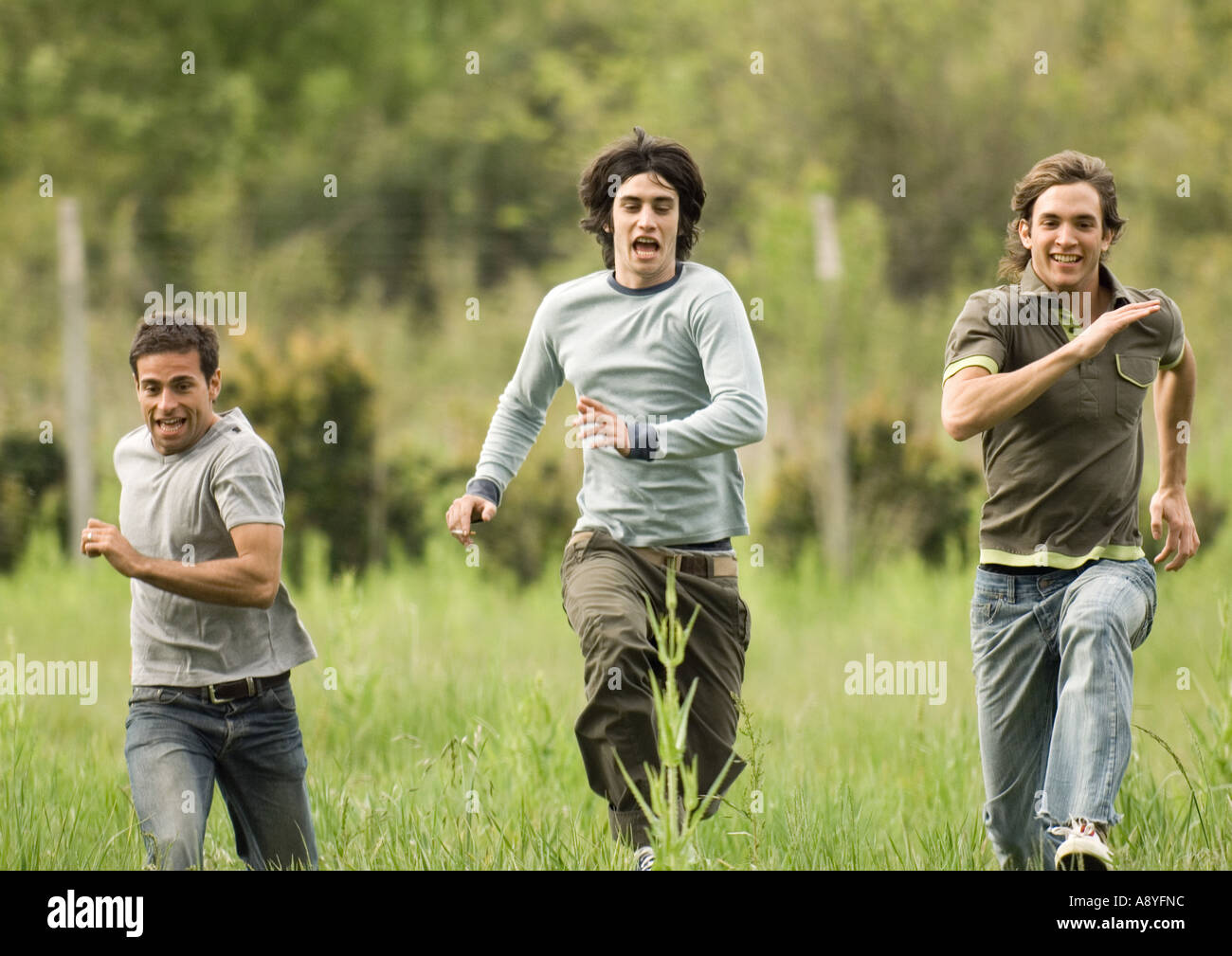 Three young male friends racing across field Stock Photo - Alamy