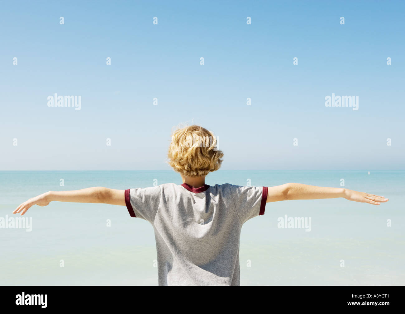Child standing facing ocean with arms straight out, rear view Stock ...