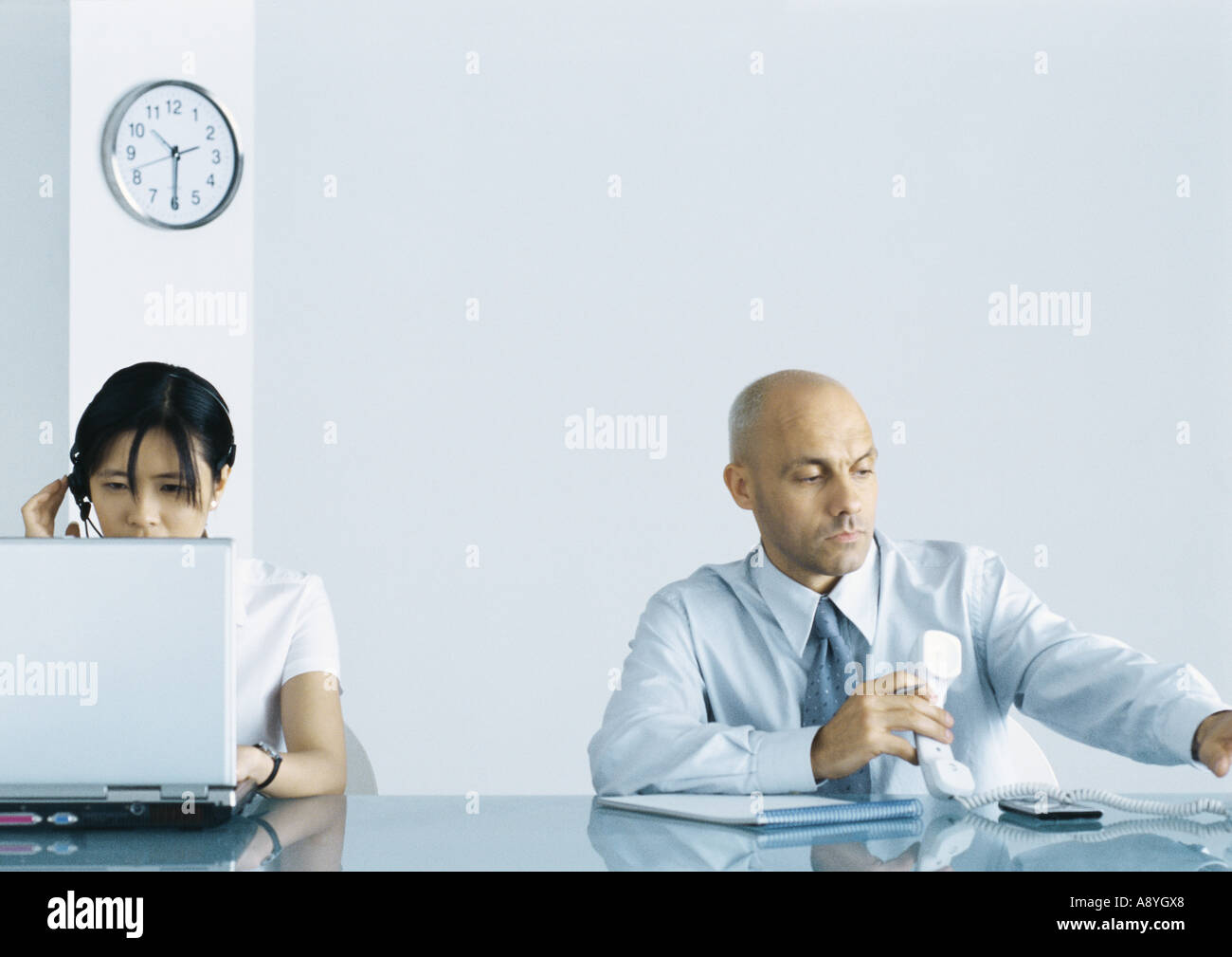 Office, man holding telephone while woman uses computer Stock Photo - Alamy
