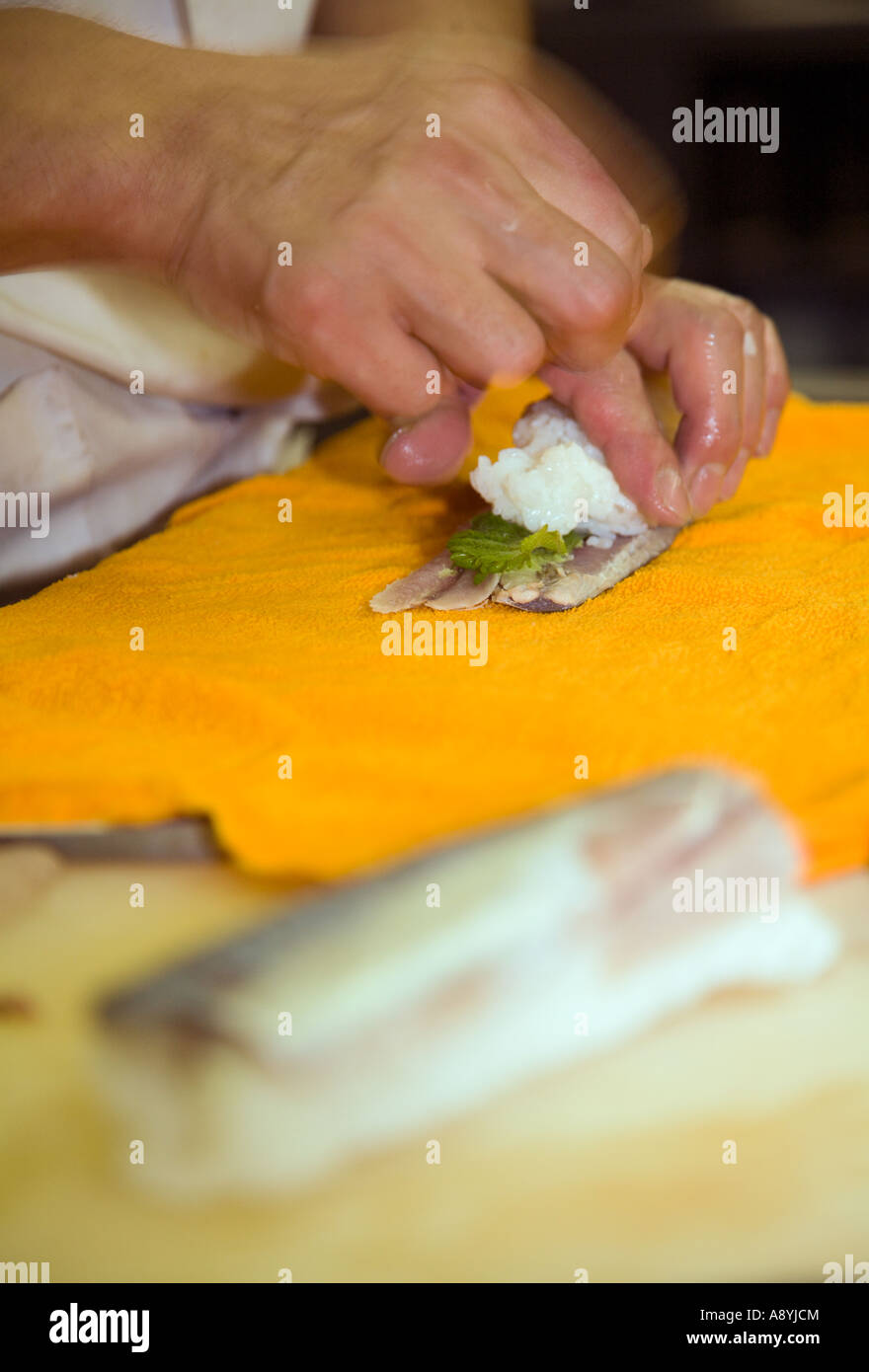 Adding rice to a layer of oba leaves while making mackerel sushi in a ...