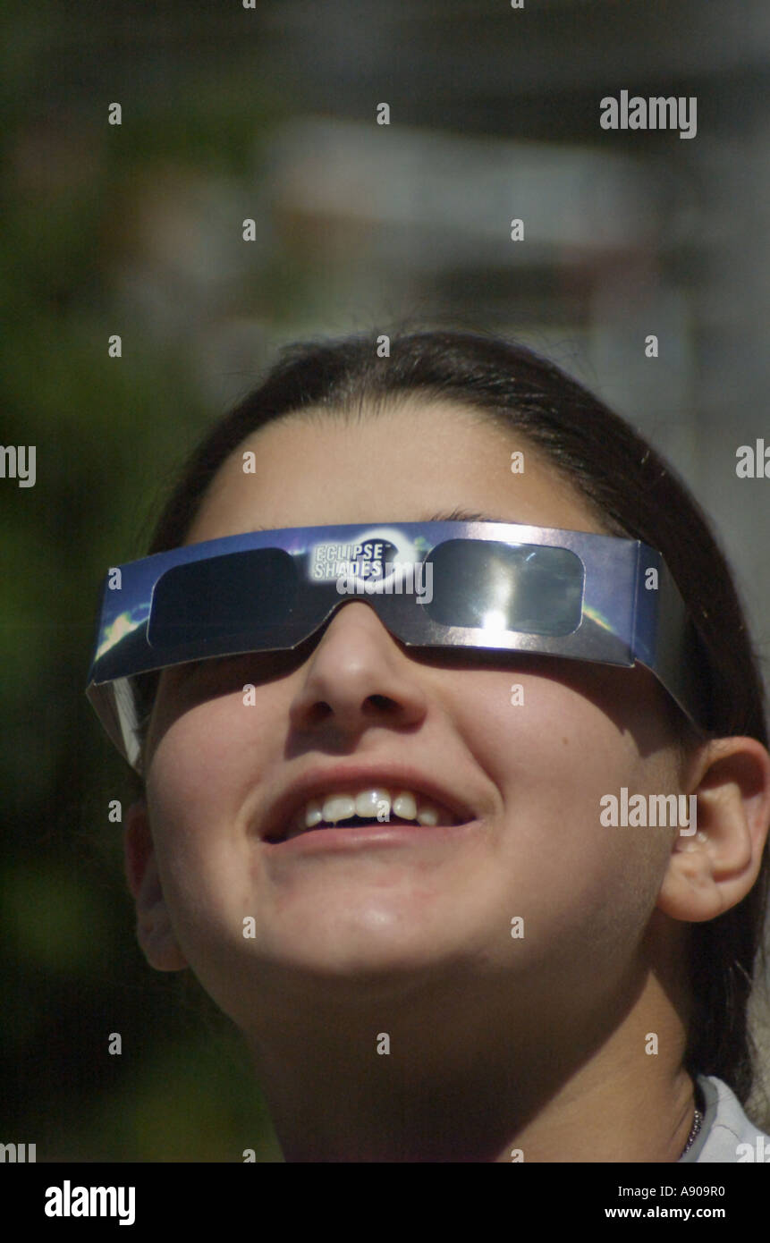a smiling young student looking at the sun with special glasses during ...
