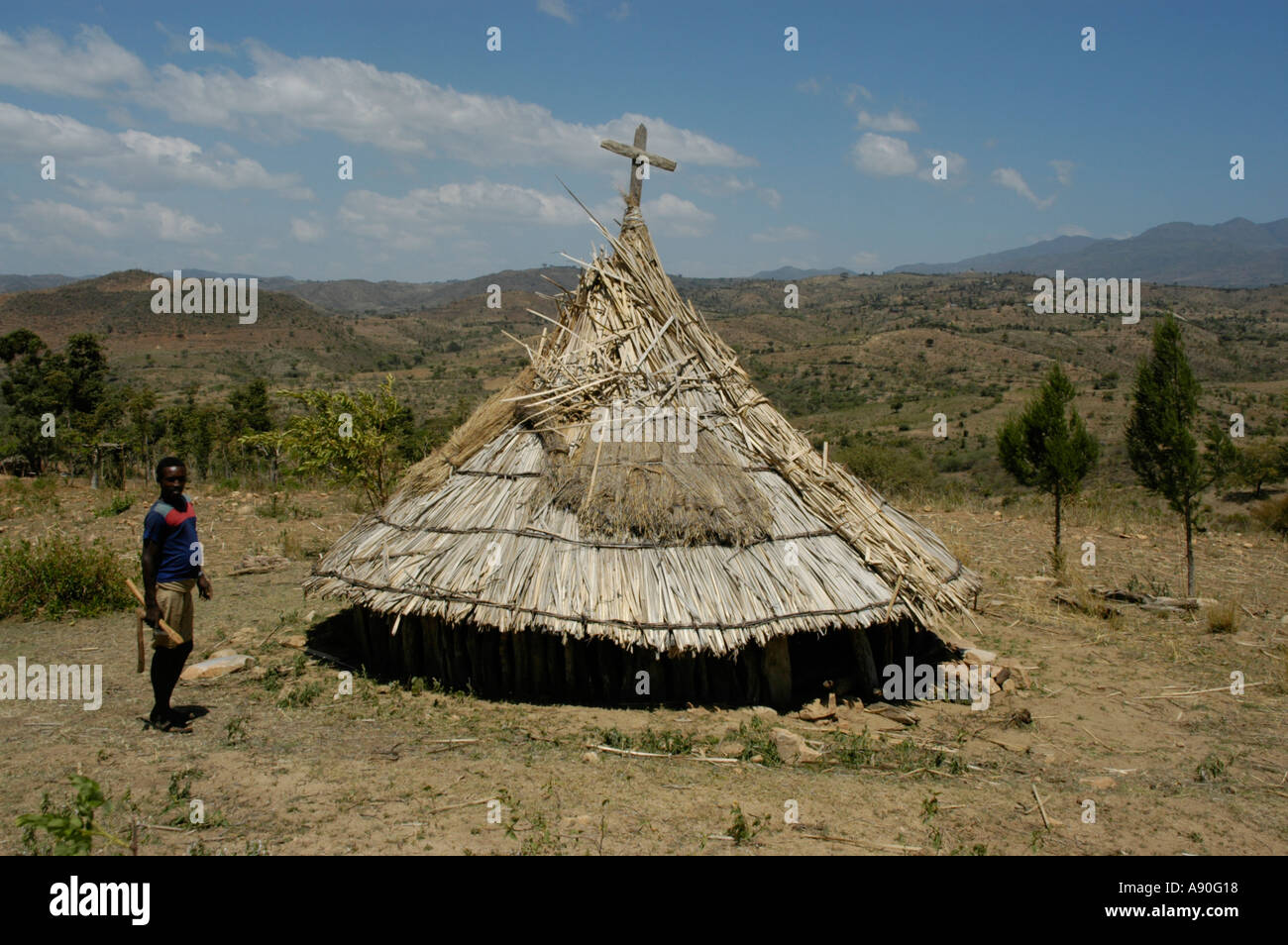A man is standing beside a Christian church like a hut with a straw ...