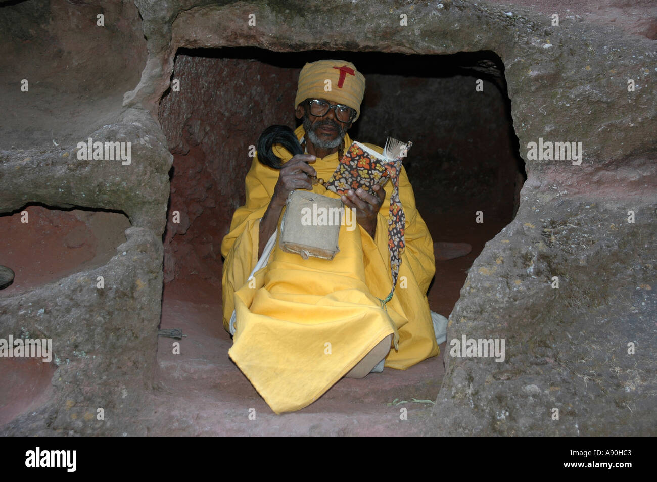 Old hermit dressed in yellow cape praying in a small rock cave rock ...
