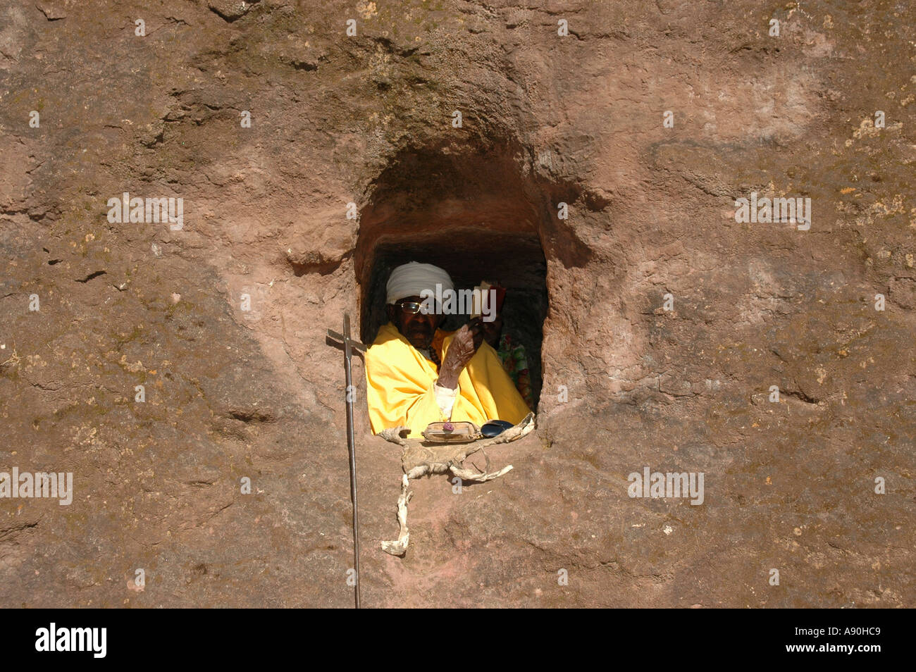 Old hermit dressed in yellow cape praying in a small rock cave rock ...