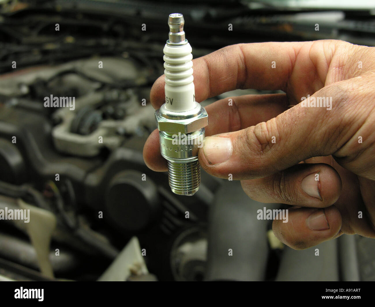 A dirty mechanics hand holding a spark plug with an engine in the ...