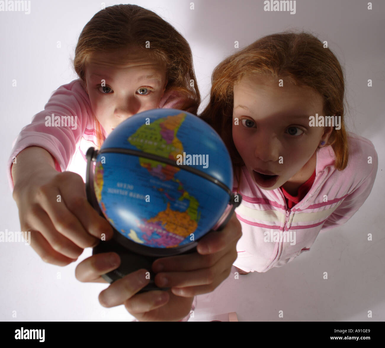 Twin sisters look at a globe together with shocked learning stance ...