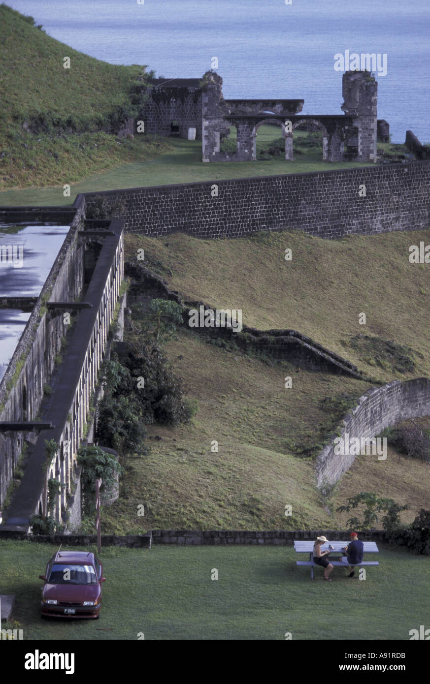 CARIBBEAN, St. Kitts, Old brick fort on side of hill, tourists sitting ...