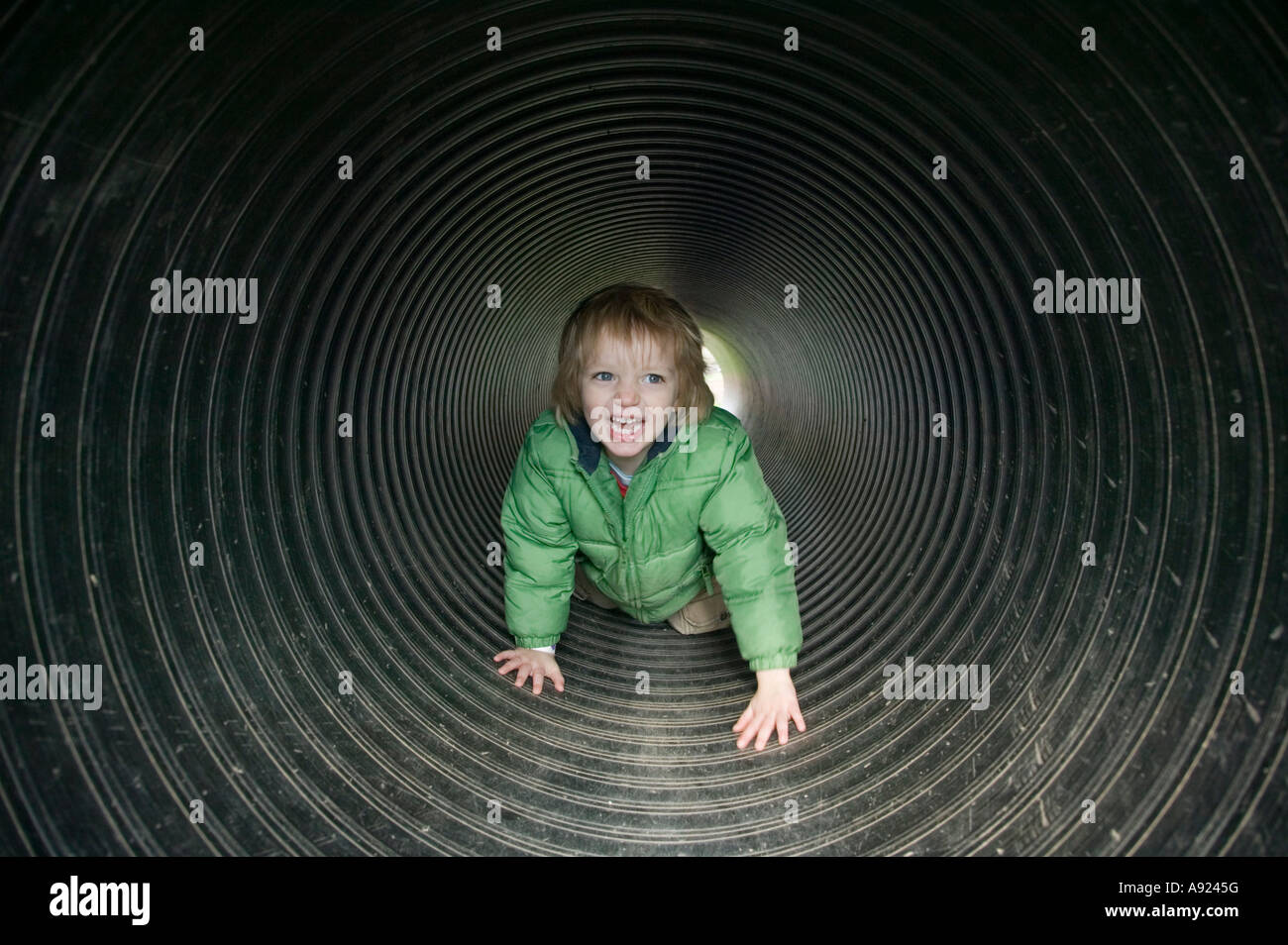 A toddler crawling through a tube at a playground Stock Photo - Alamy