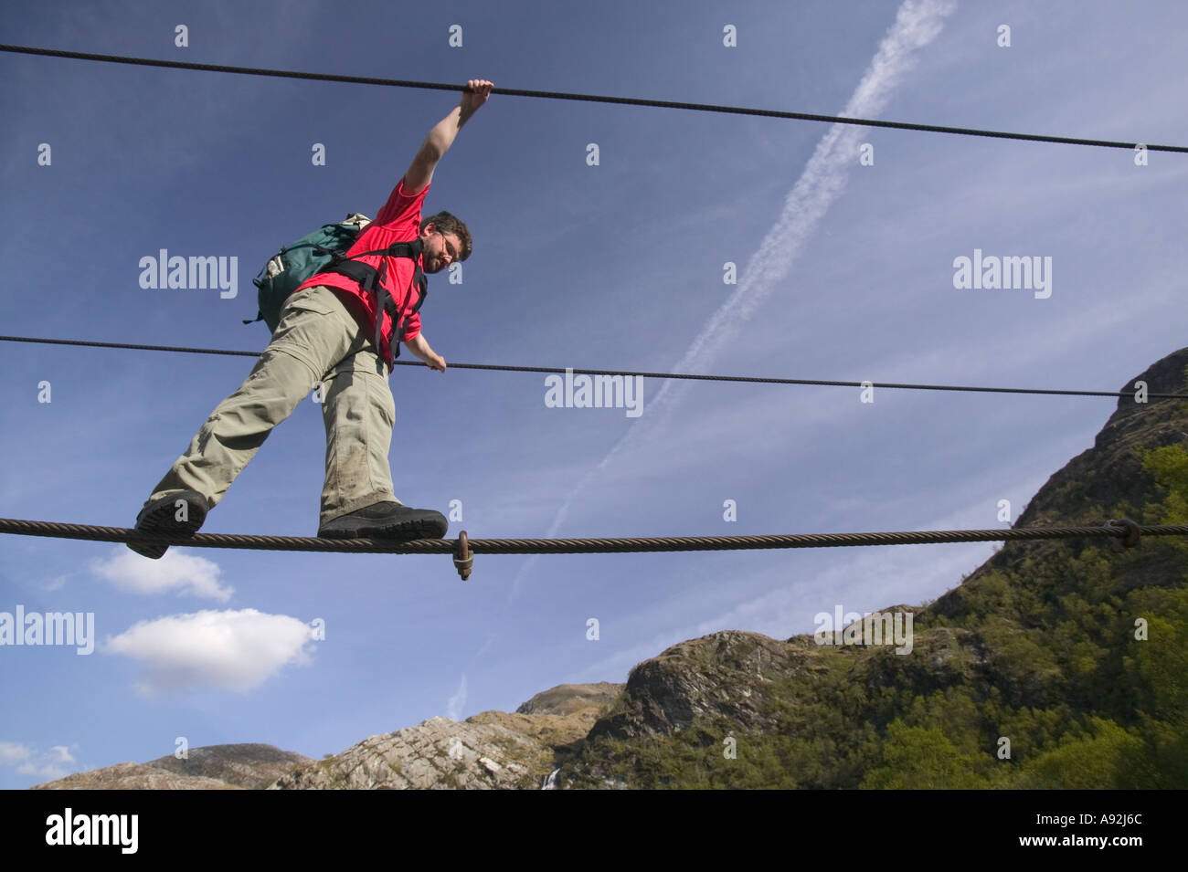 a climber crosses the rope bridge in glen Nevis at Steall Falls Stock ...