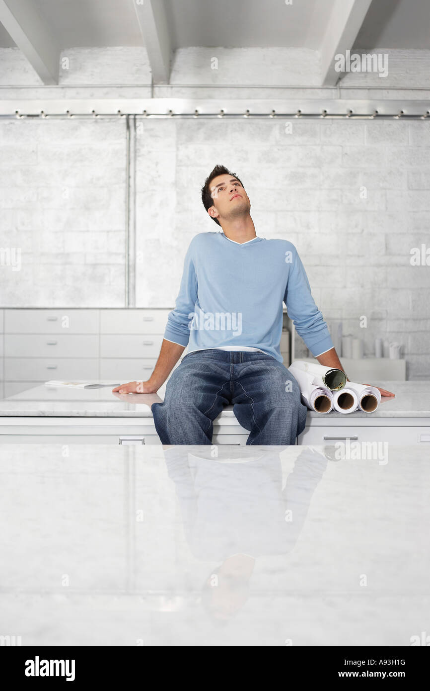 Young man sitting on desk, looking up Stock Photo - Alamy