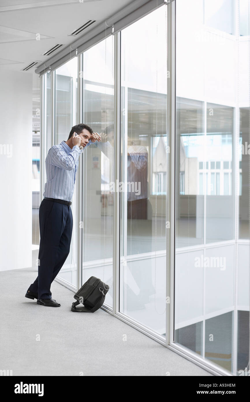 Office worker talking on mobile phone, looking out window of empty ...