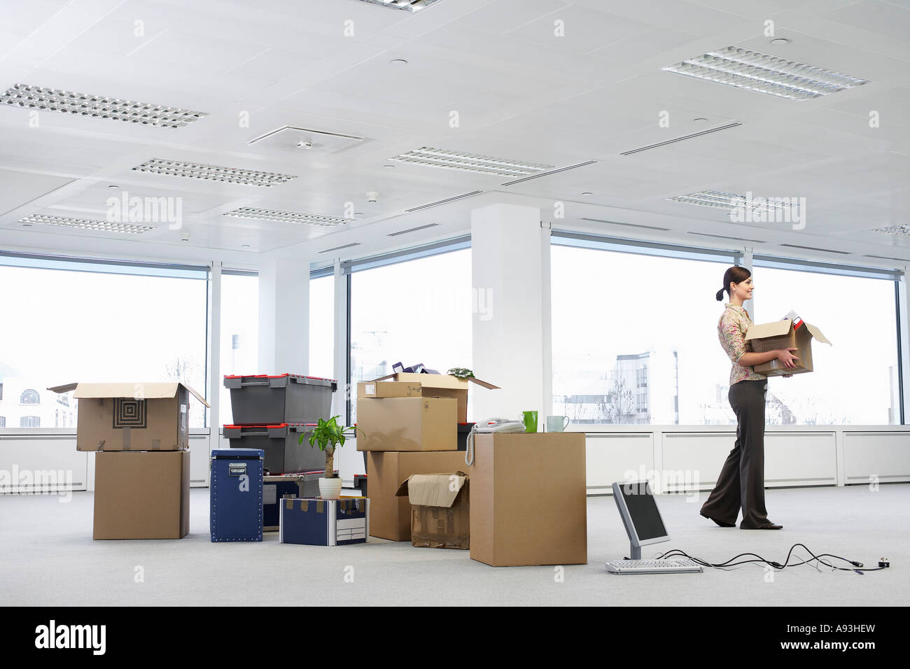 Office worker carrying carton near cartons and equipment on floor of ...