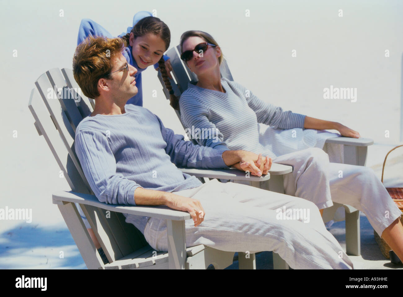 Parents sitting in adirondack chairs with their daughter standing ...