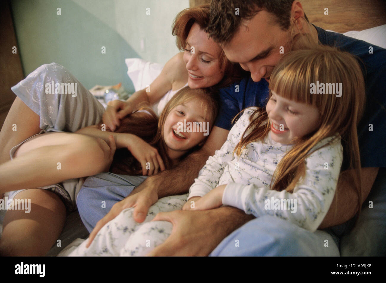 Parents hugging their daughters in bed Stock Photo - Alamy