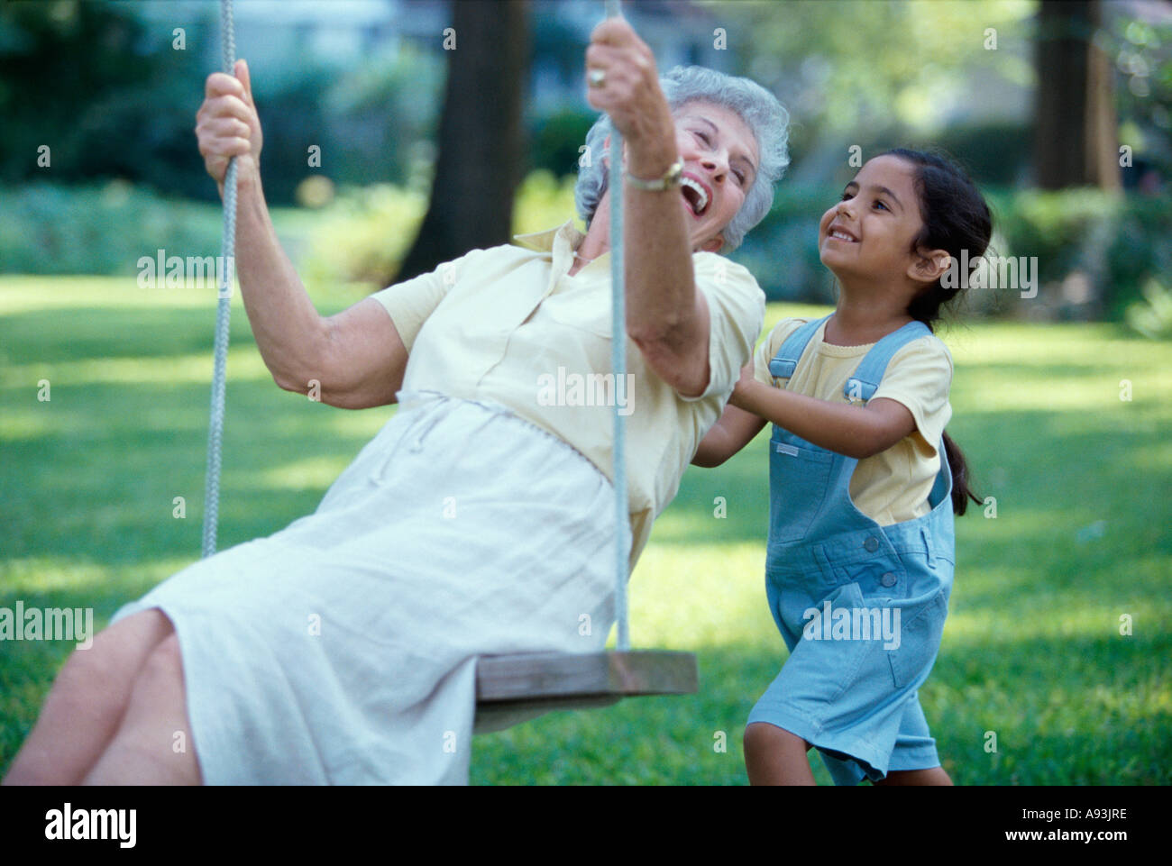 Side profile of a granddaughter pushing her grandmother on a swing ...