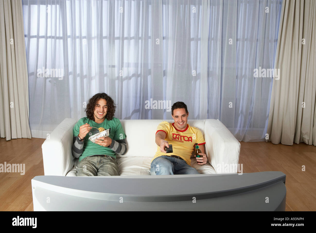 Two men sitting on sofa, watching television Stock Photo - Alamy