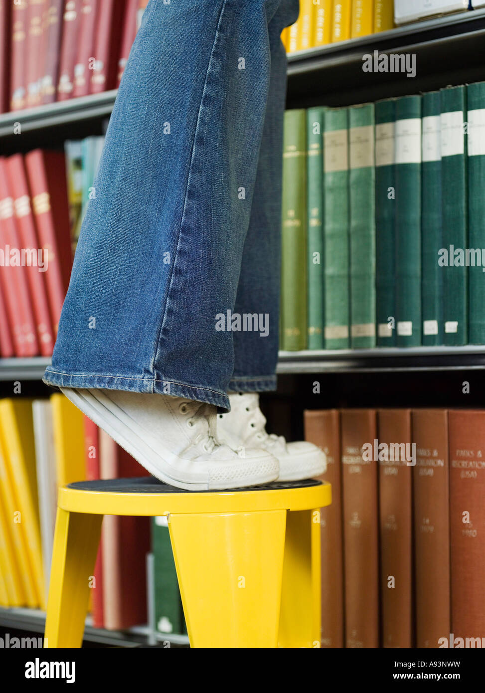 Young woman standing on stool, reaching for book, low section Stock ...