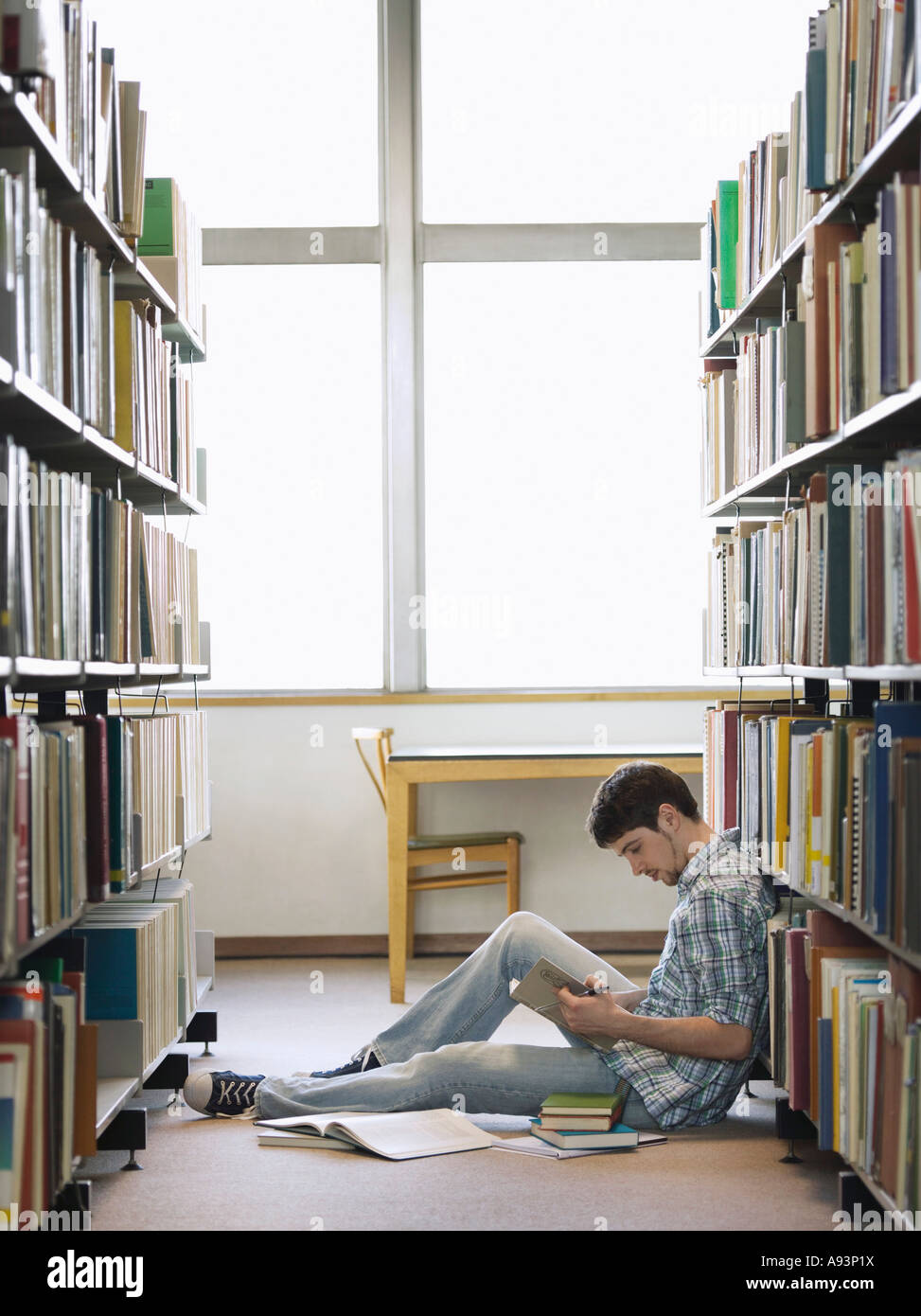 Student reading sitting on floor in library Stock Photo - Alamy