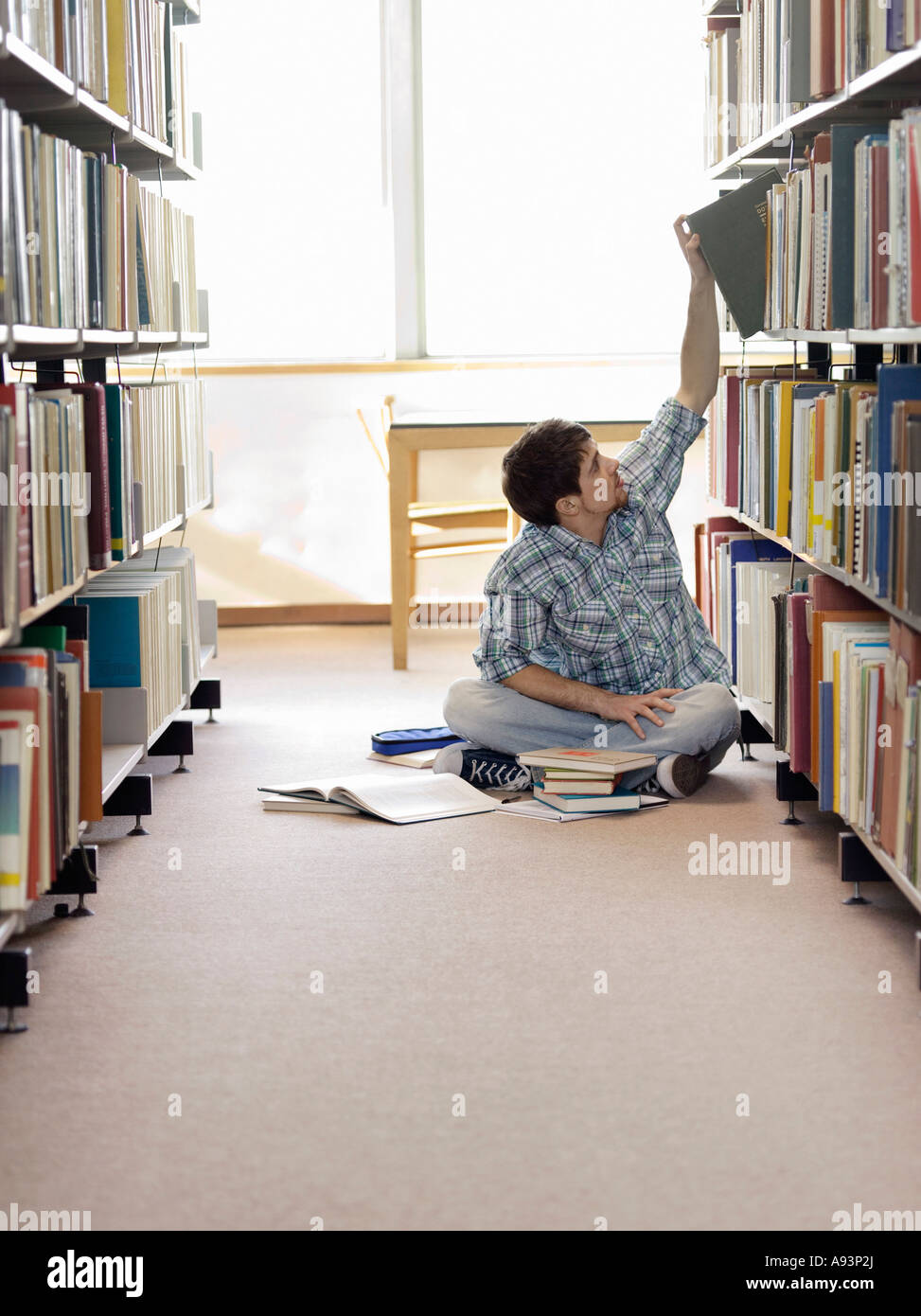 Student sitting on floor in library, reaching for book Stock Photo - Alamy