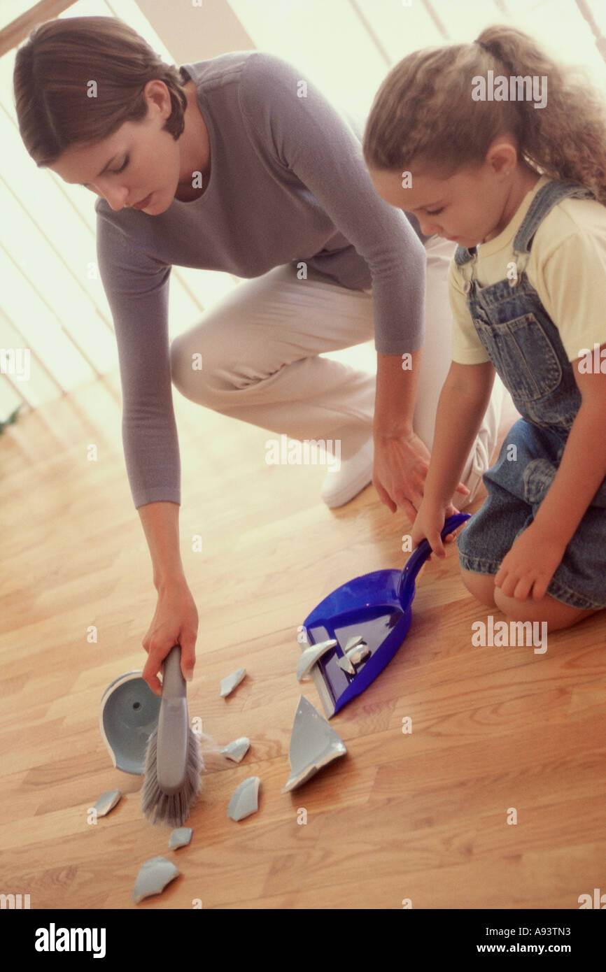 Daughter helping her mother sweep the pieces of broken crockery off the ...