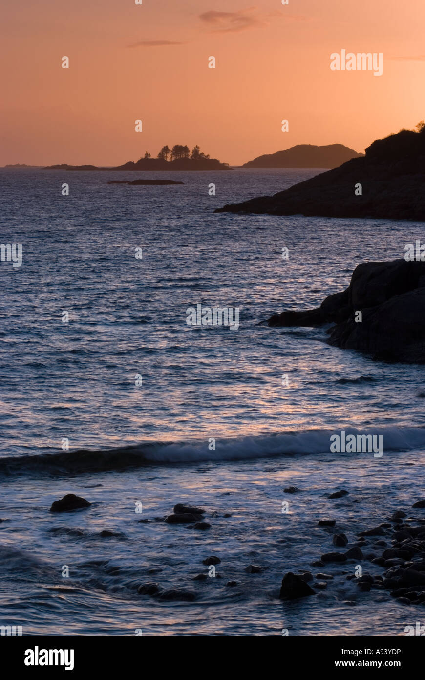 Misty waves crash upon a rocky pebble beach at sunset creating eery ...