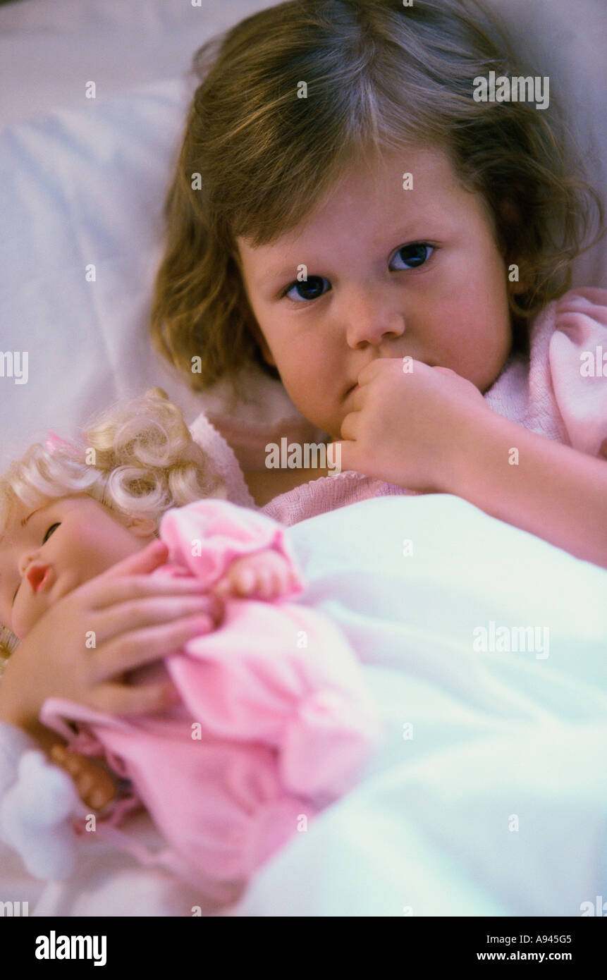 Portrait of a baby girl with a doll lying in bed Stock Photo - Alamy