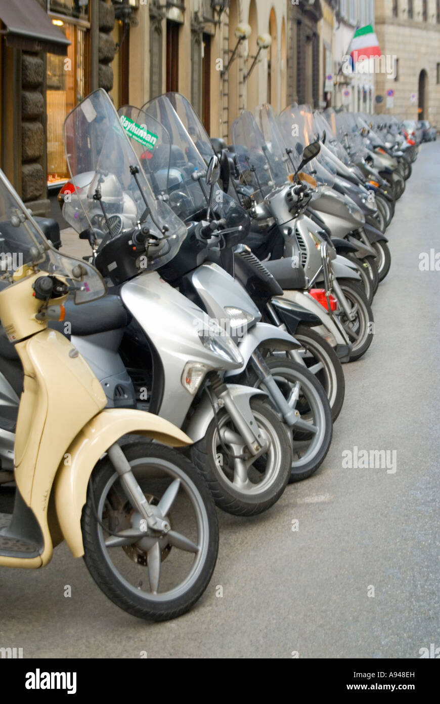 Vertical close up of a row of many mopeds and scooters parked on the ...