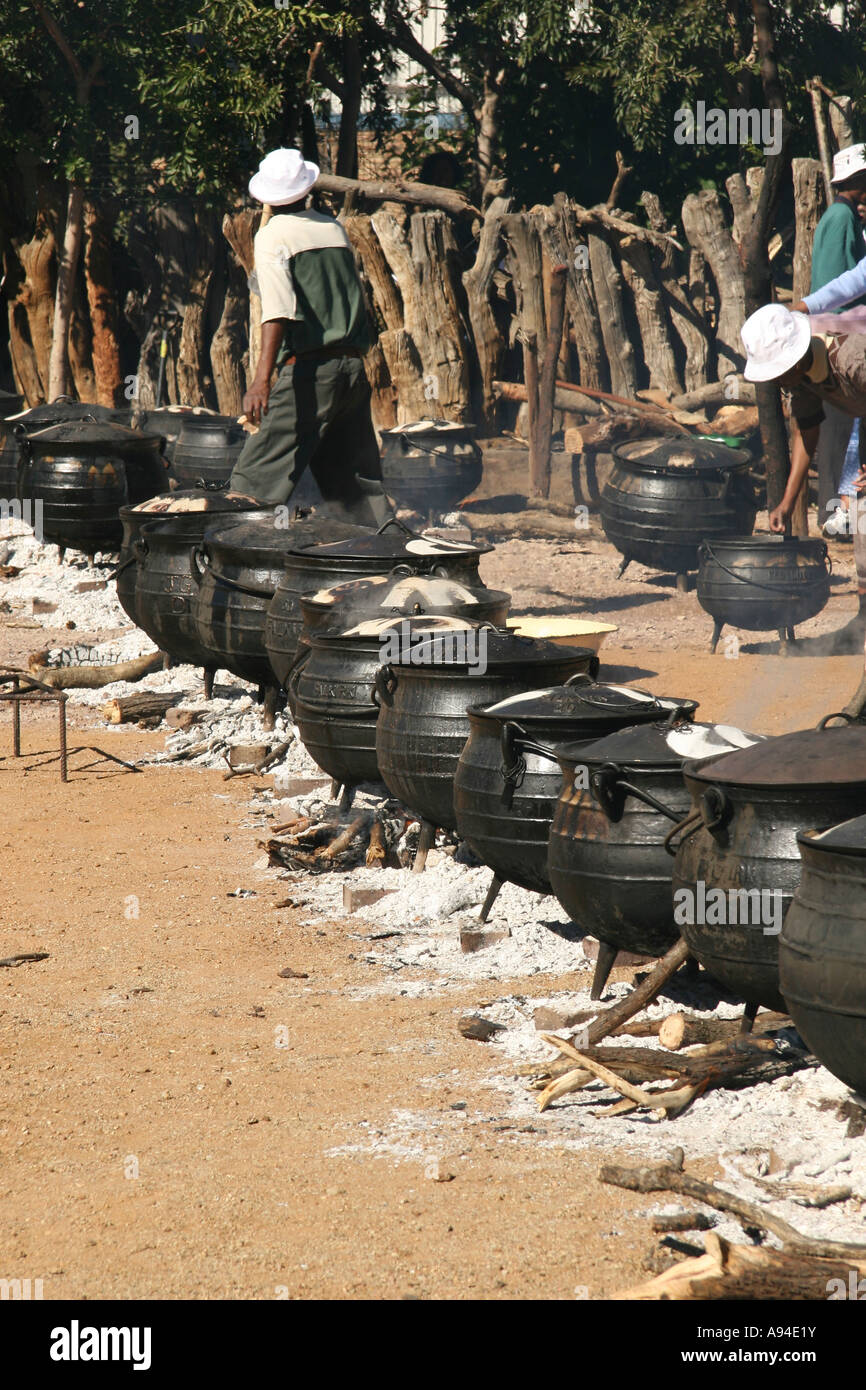 Traditional food being prepared in a row of three legged iron cooking ...