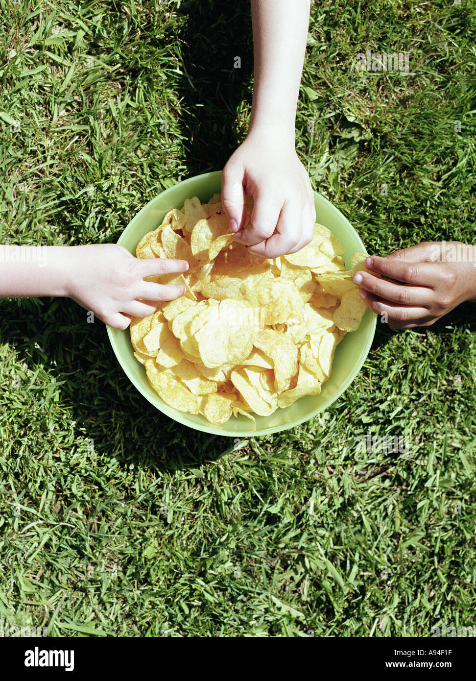 three children dipping their hands into a bowl of potato chips Stock ...