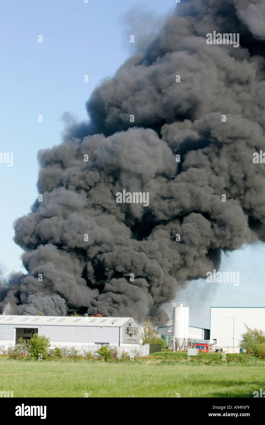 huge vertical plume of black grey smoke rising from industrial building fire at medical ...