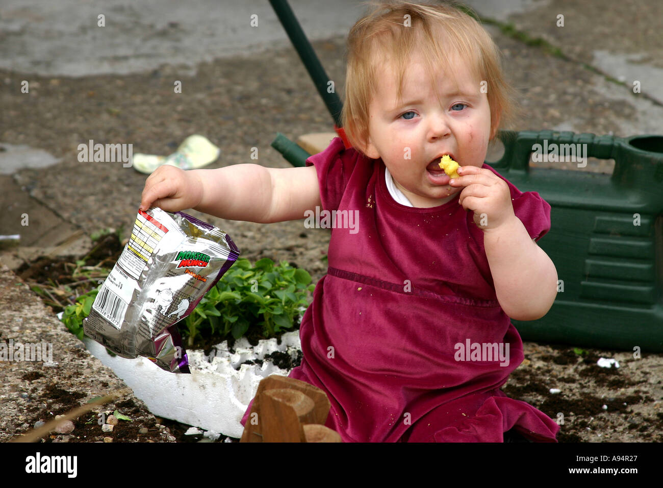 Little girl eating crisps from a packet and sitting in the middle of ...