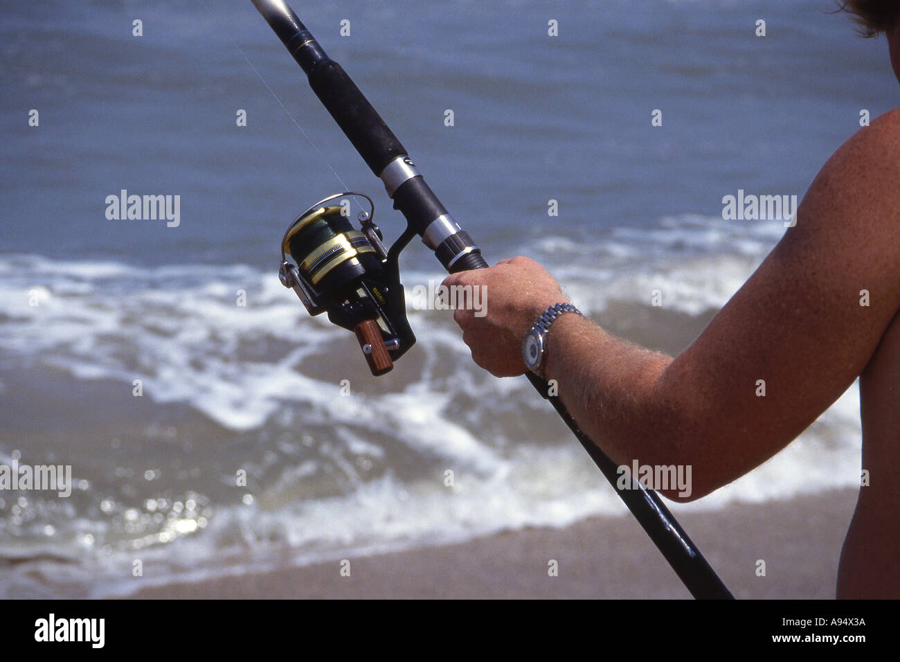 Hand holding fishing rod and showing reel with sea behind Stock Photo ...