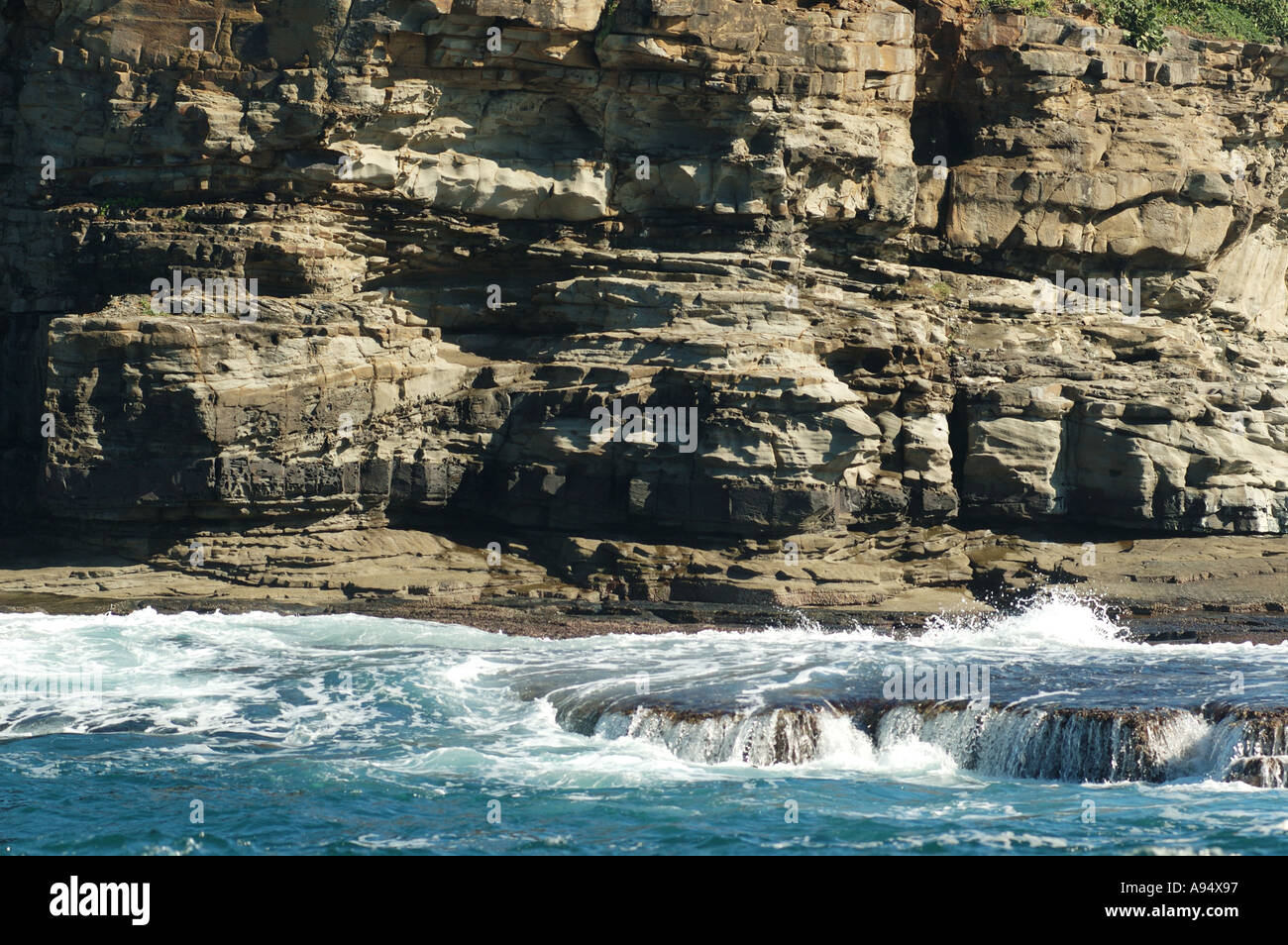 Waves break on rock shelf at the base of a cliff Stock Photo - Alamy