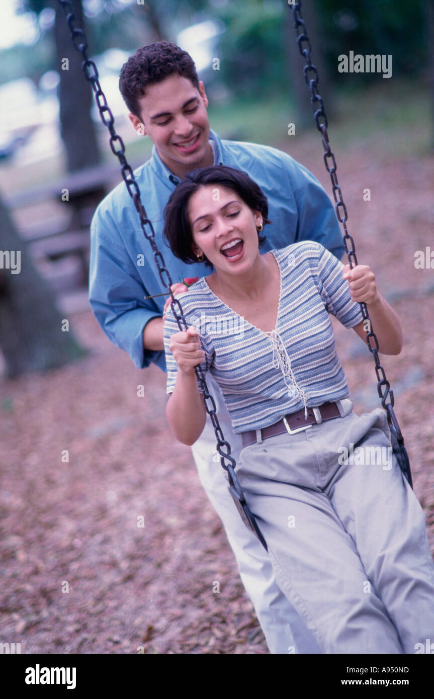 Young man pushing a young woman on a swing Stock Photo - Alamy