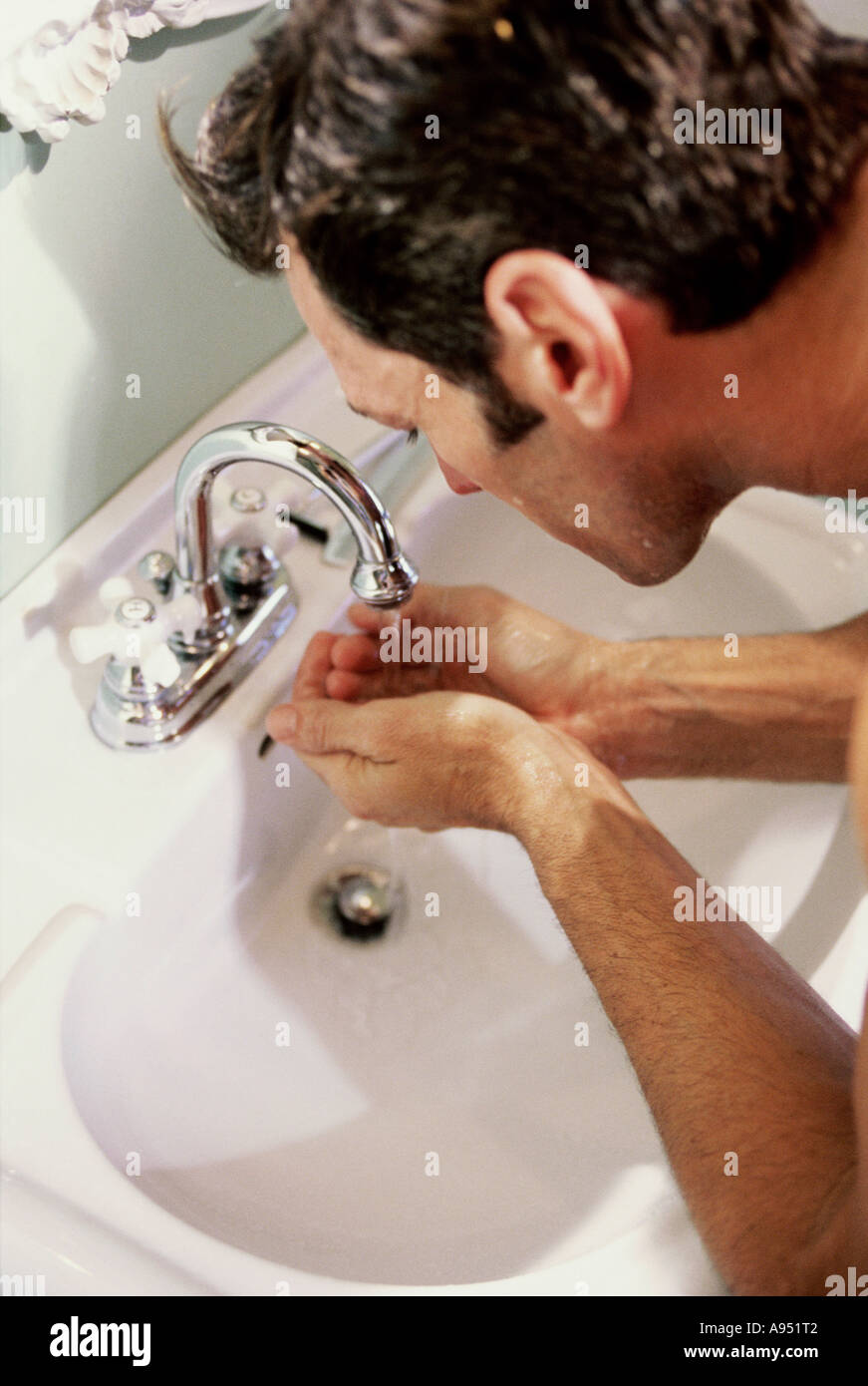 High angle view of a young man washing his face in the bathroom sink ...