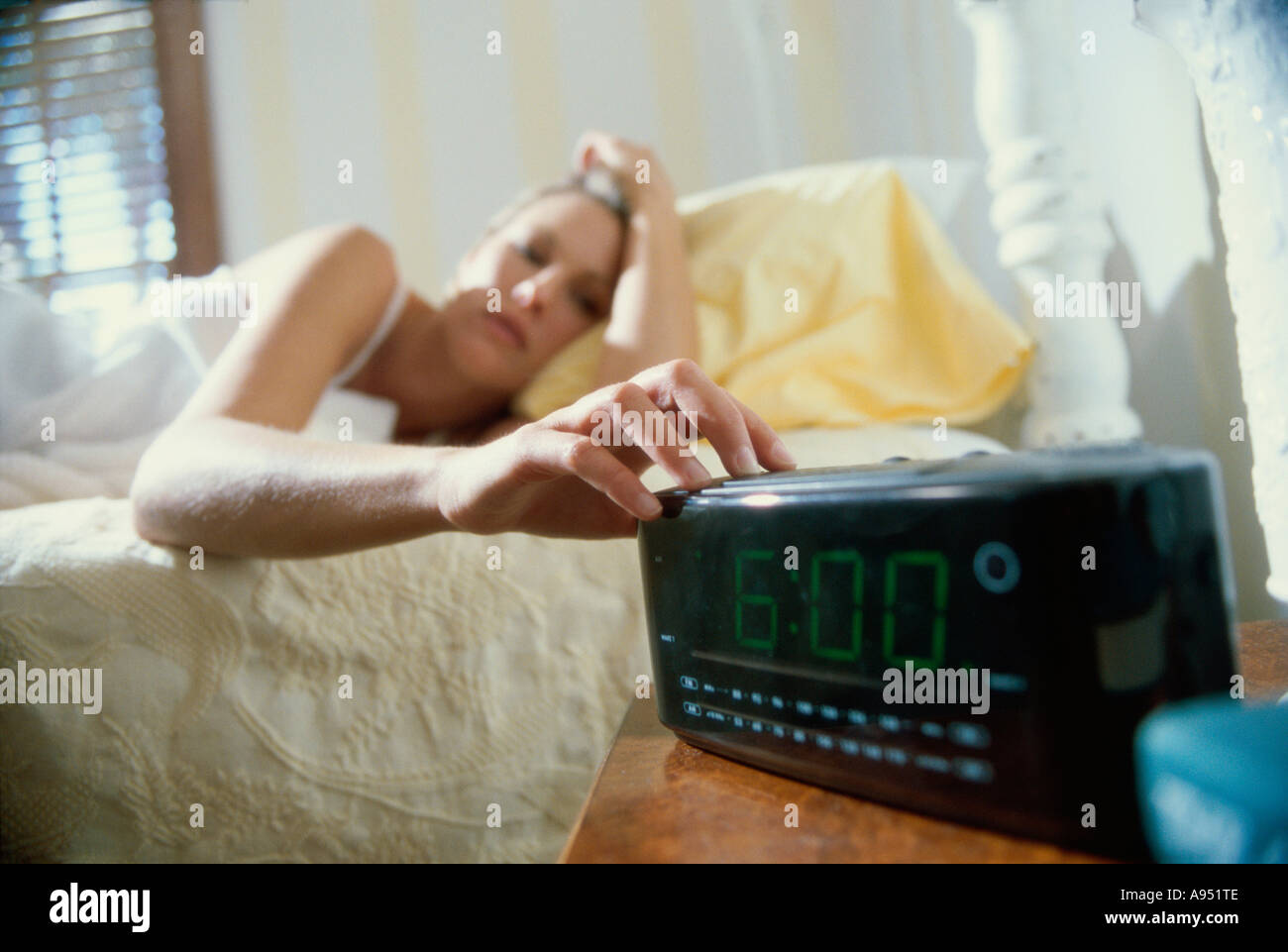 Young woman lying in bed reaching for an alarm clock Stock Photo - Alamy