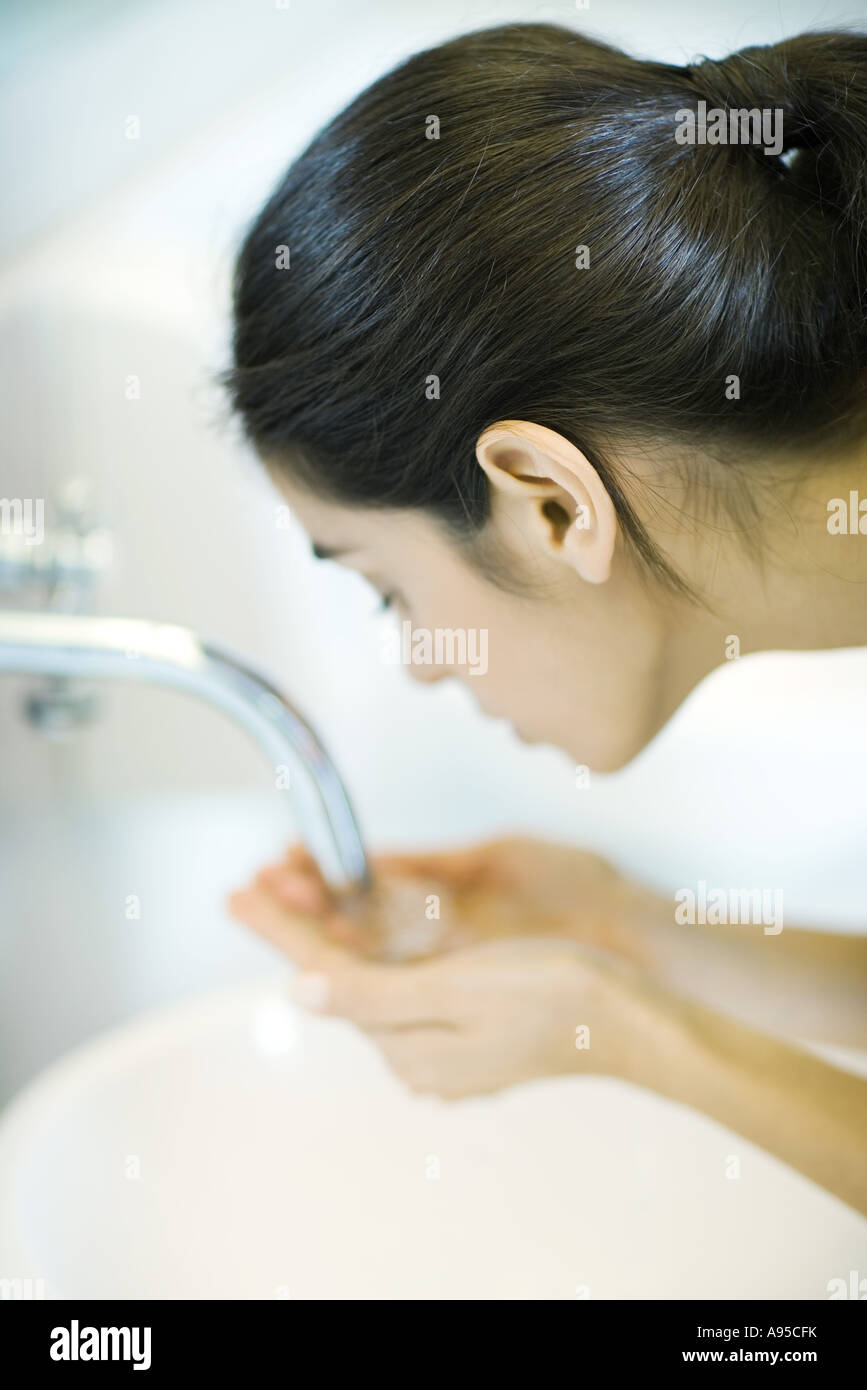 Young woman leaning over sink, hands cupped under faucet Stock Photo ...